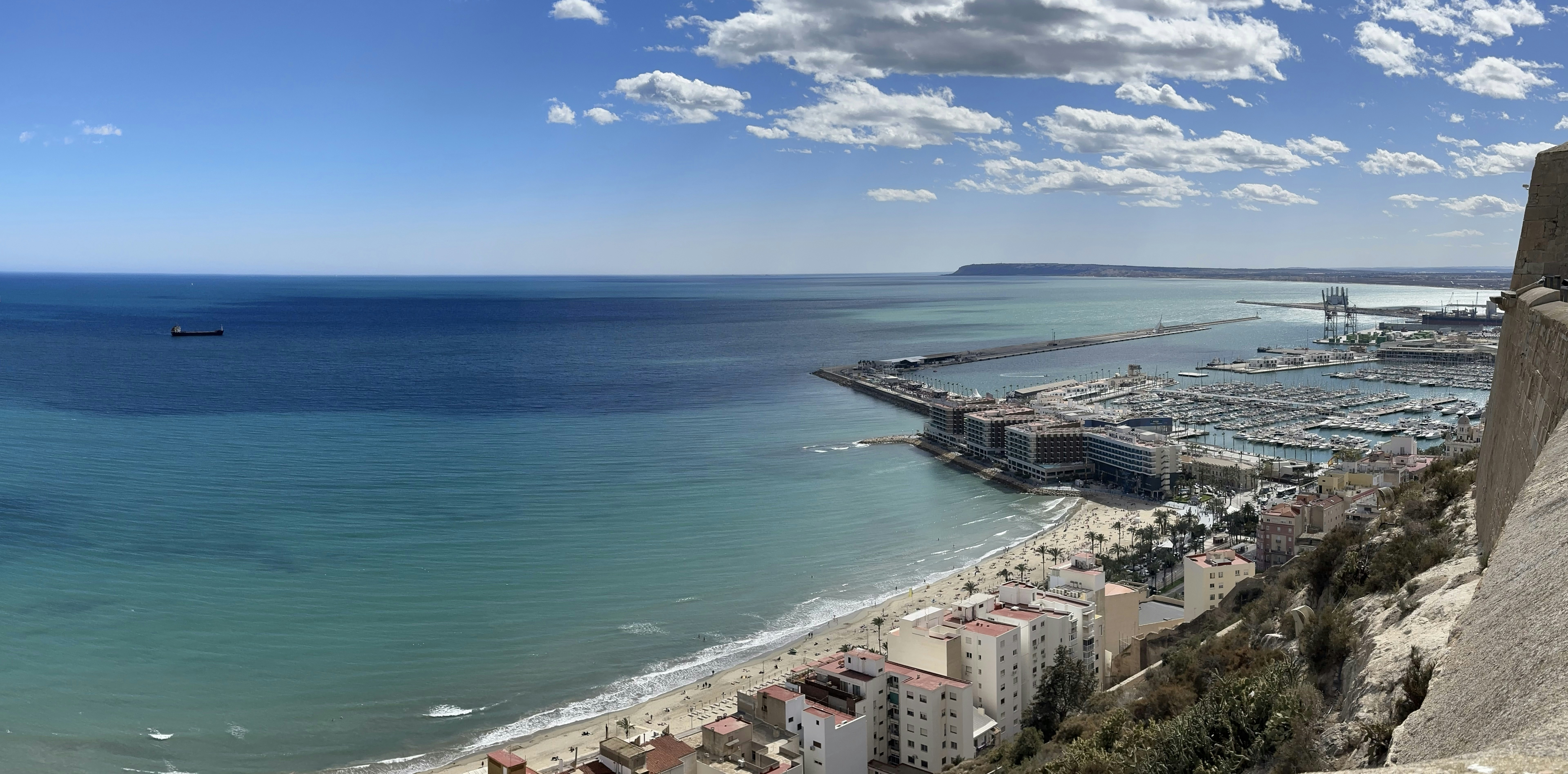 Coastal view of Alicante with turquoise waters meeting the cityscape under a vibrant sky.