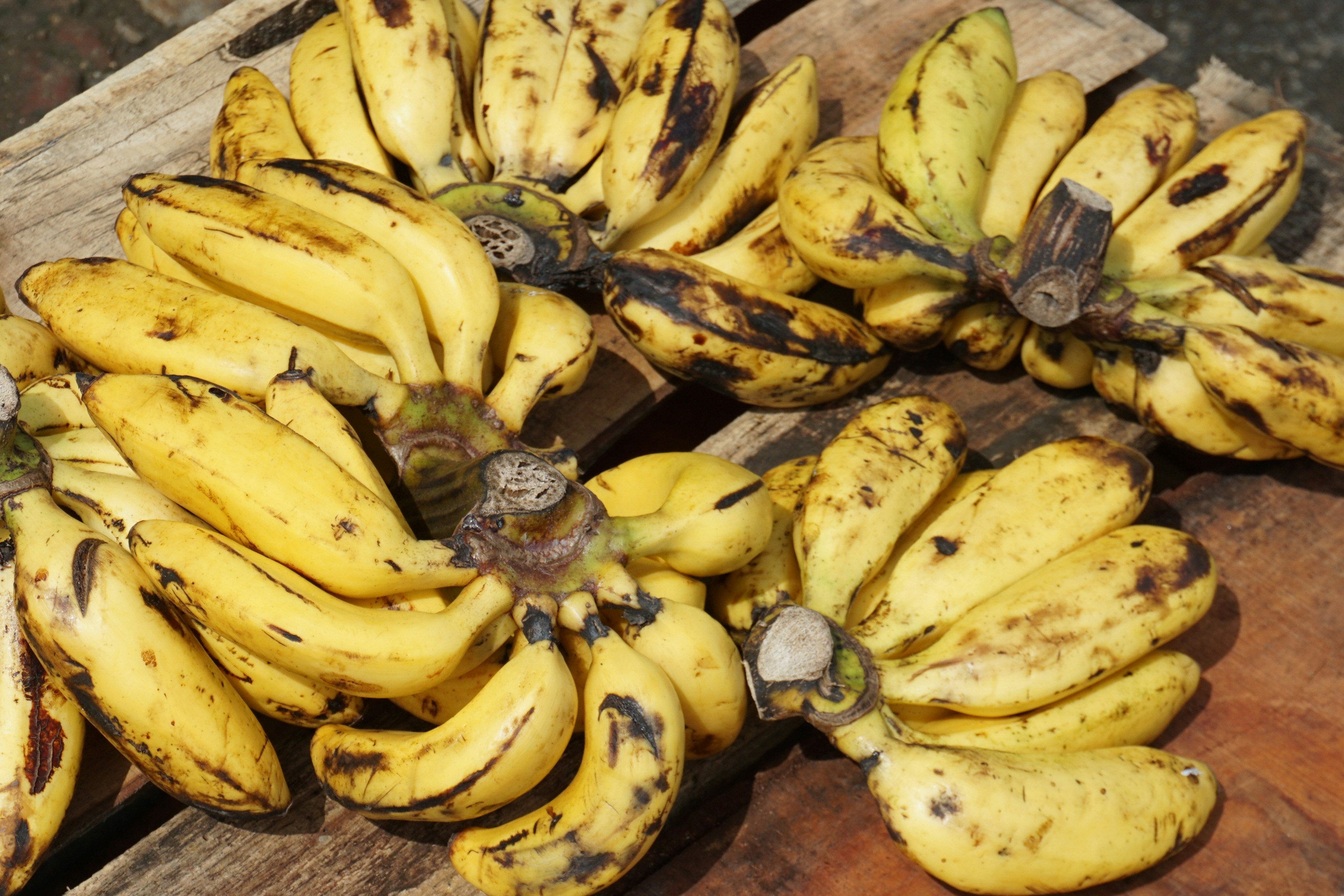 Clusters of ripe yellow bananas with dark spots on wooden crates.
