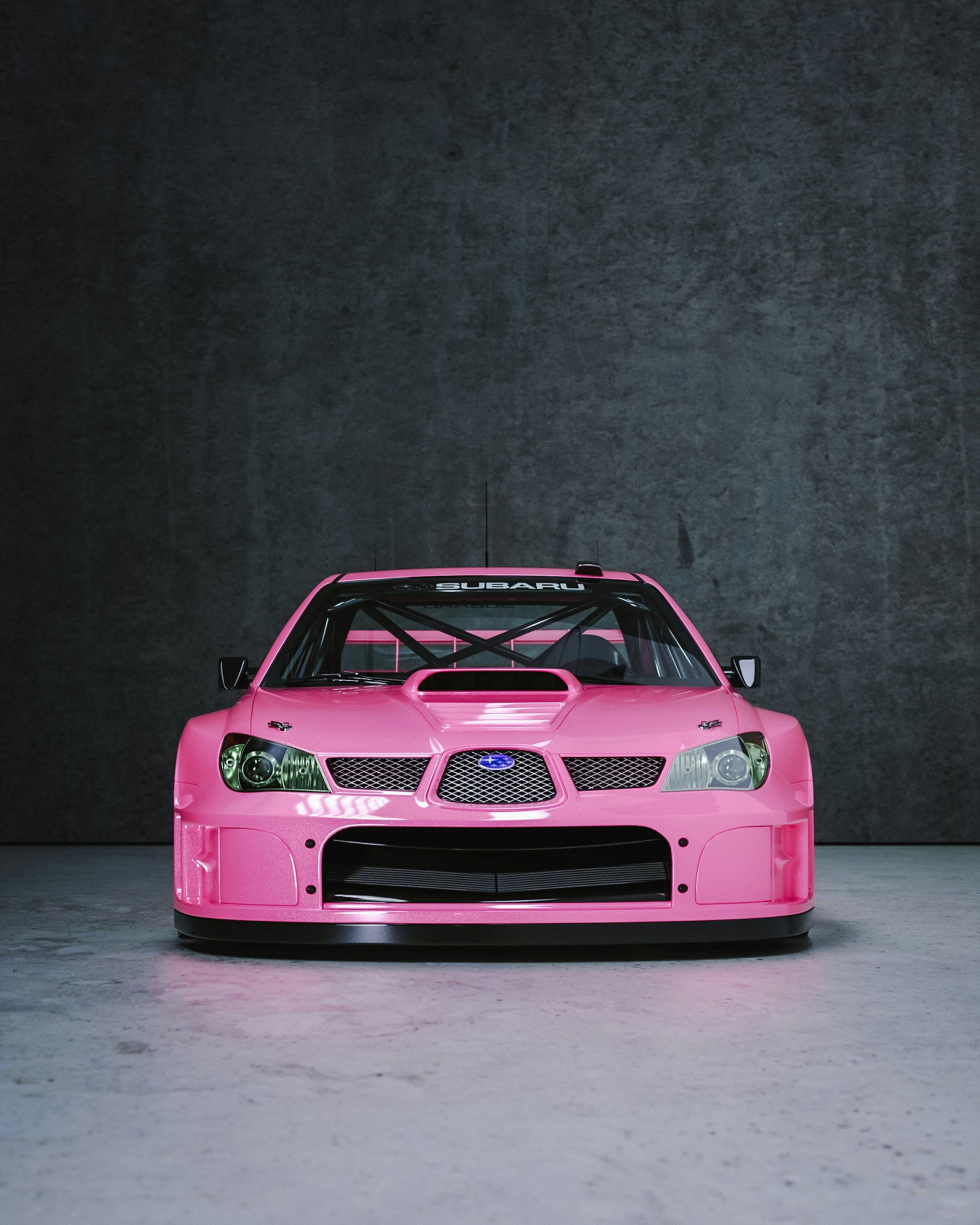 A pink subaru race car parked in front of a wall. photo – Free Digital ...