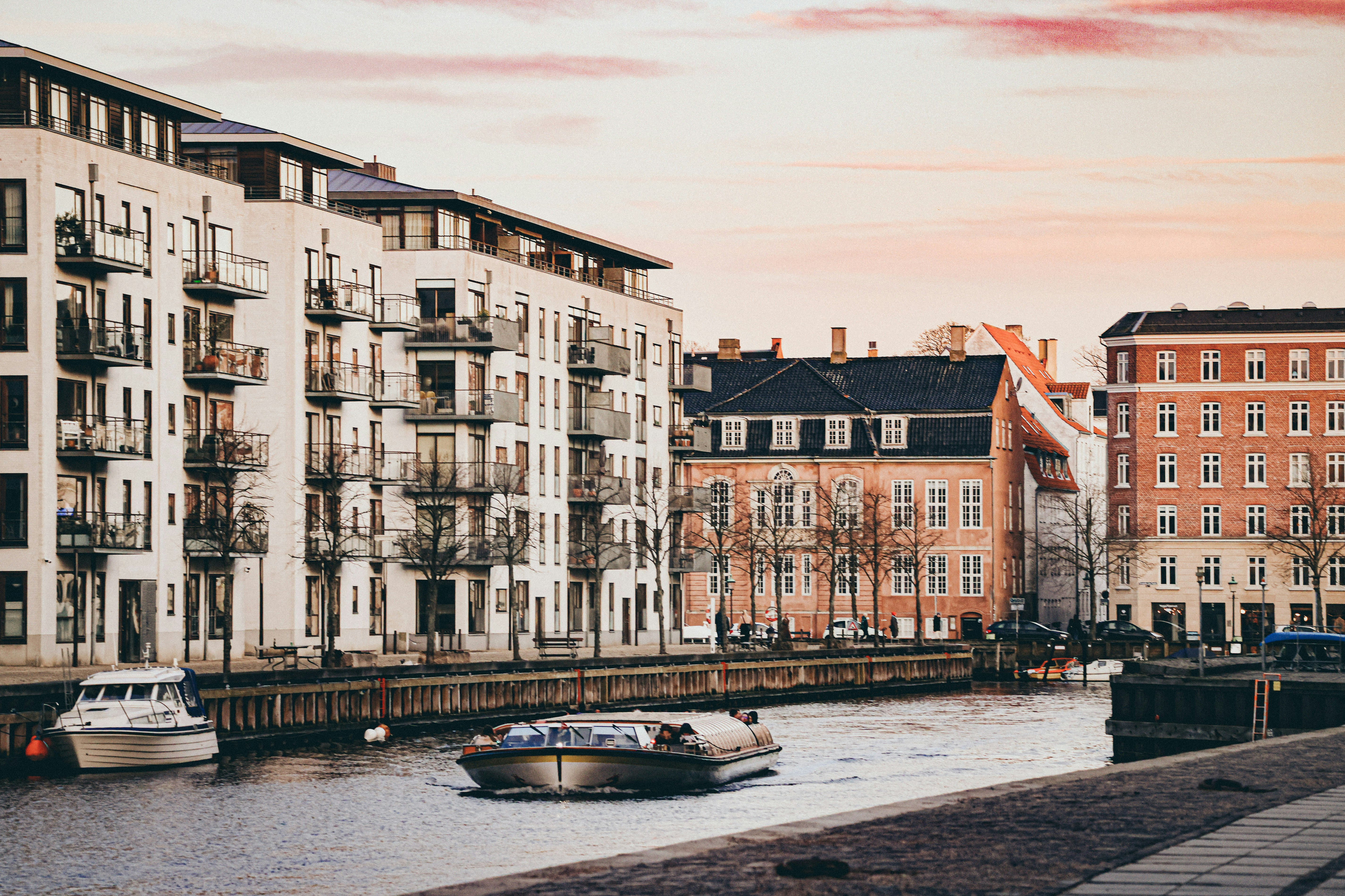Boat cruising through a canal lined with modern and historical buildings under a pastel sky.