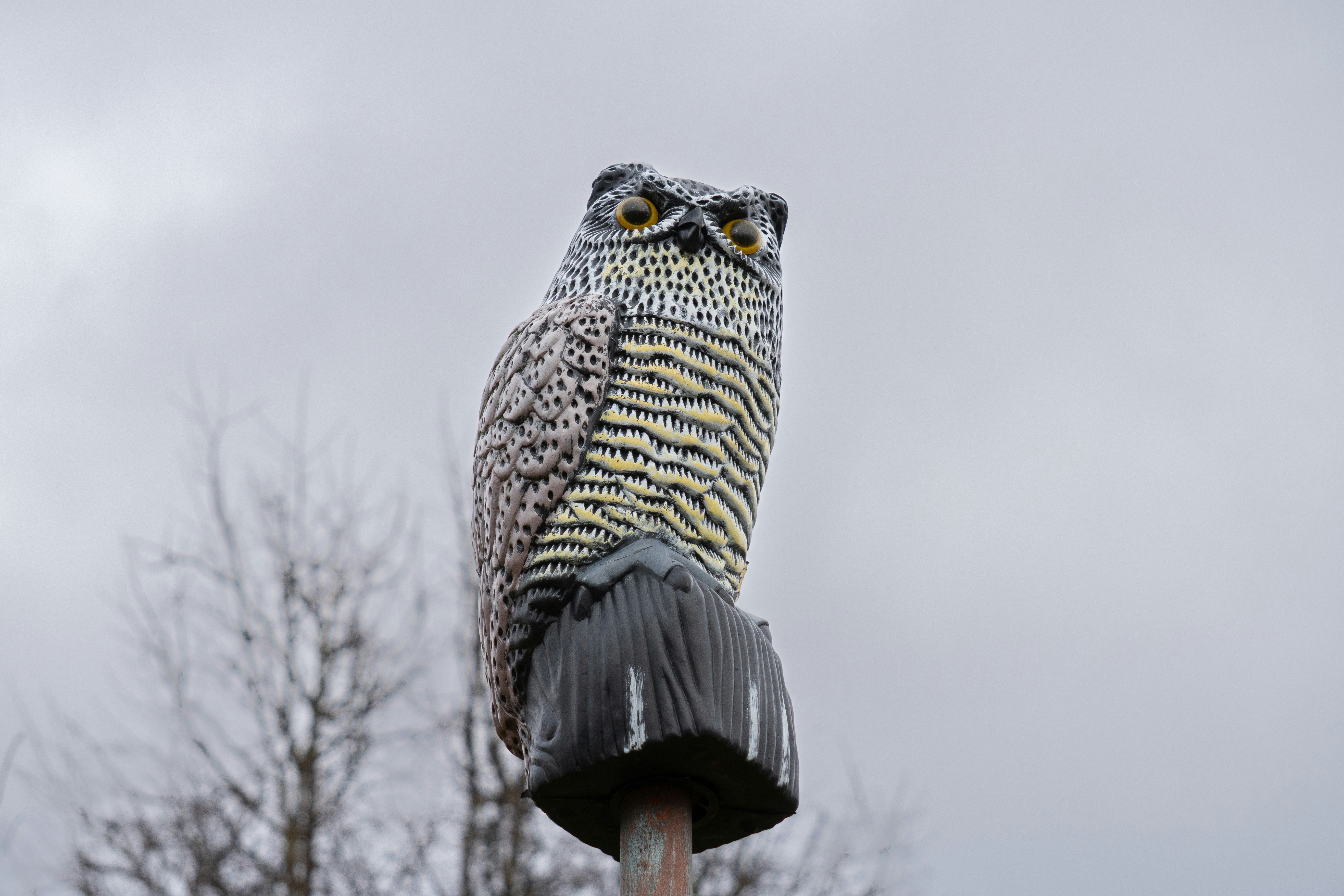 Carved owl sculpture perched high with gray clouds in the background.