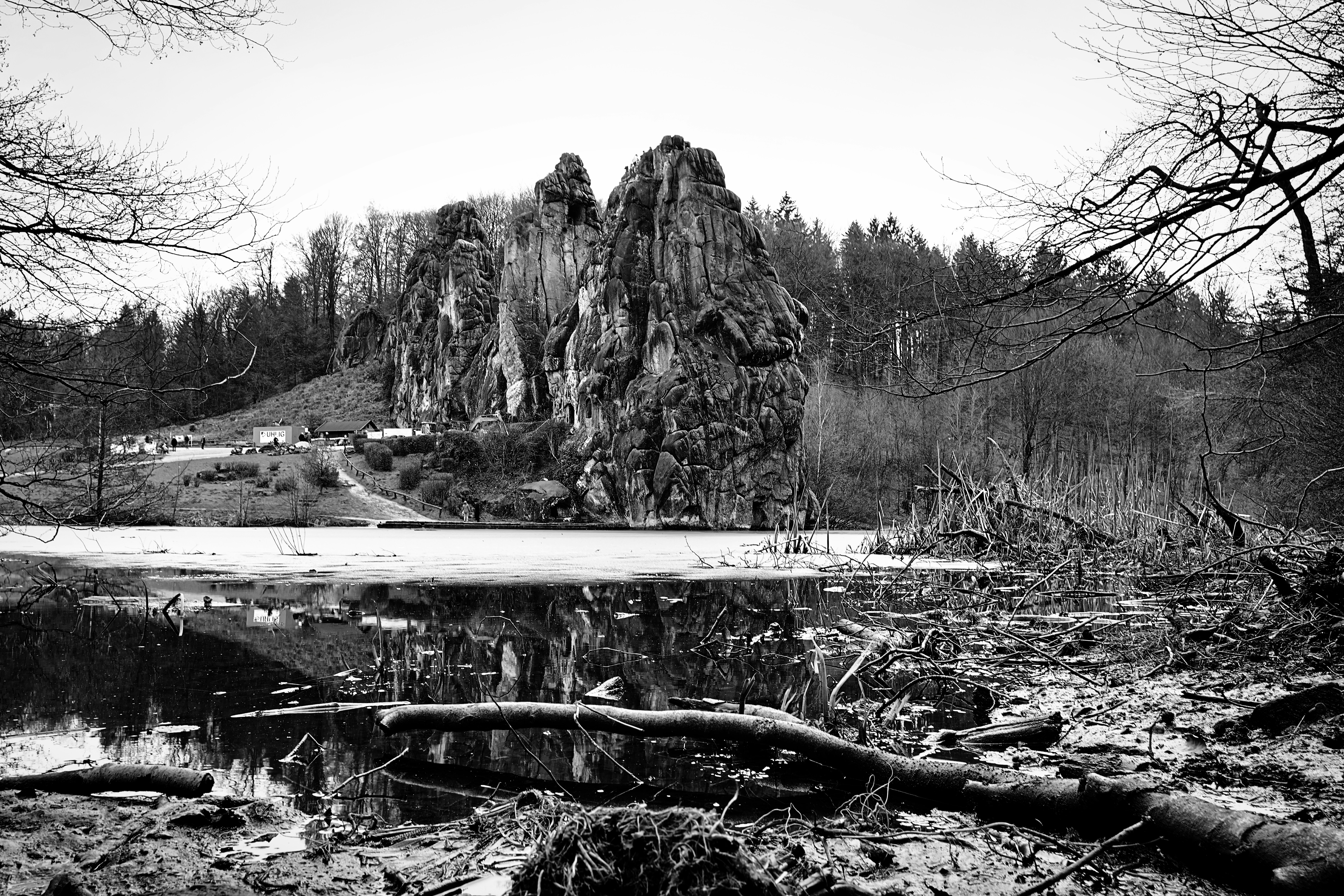 Monolithic rock formations rise above a tranquil lake, surrounded by winter-bare trees and mirrored in the water's surface.