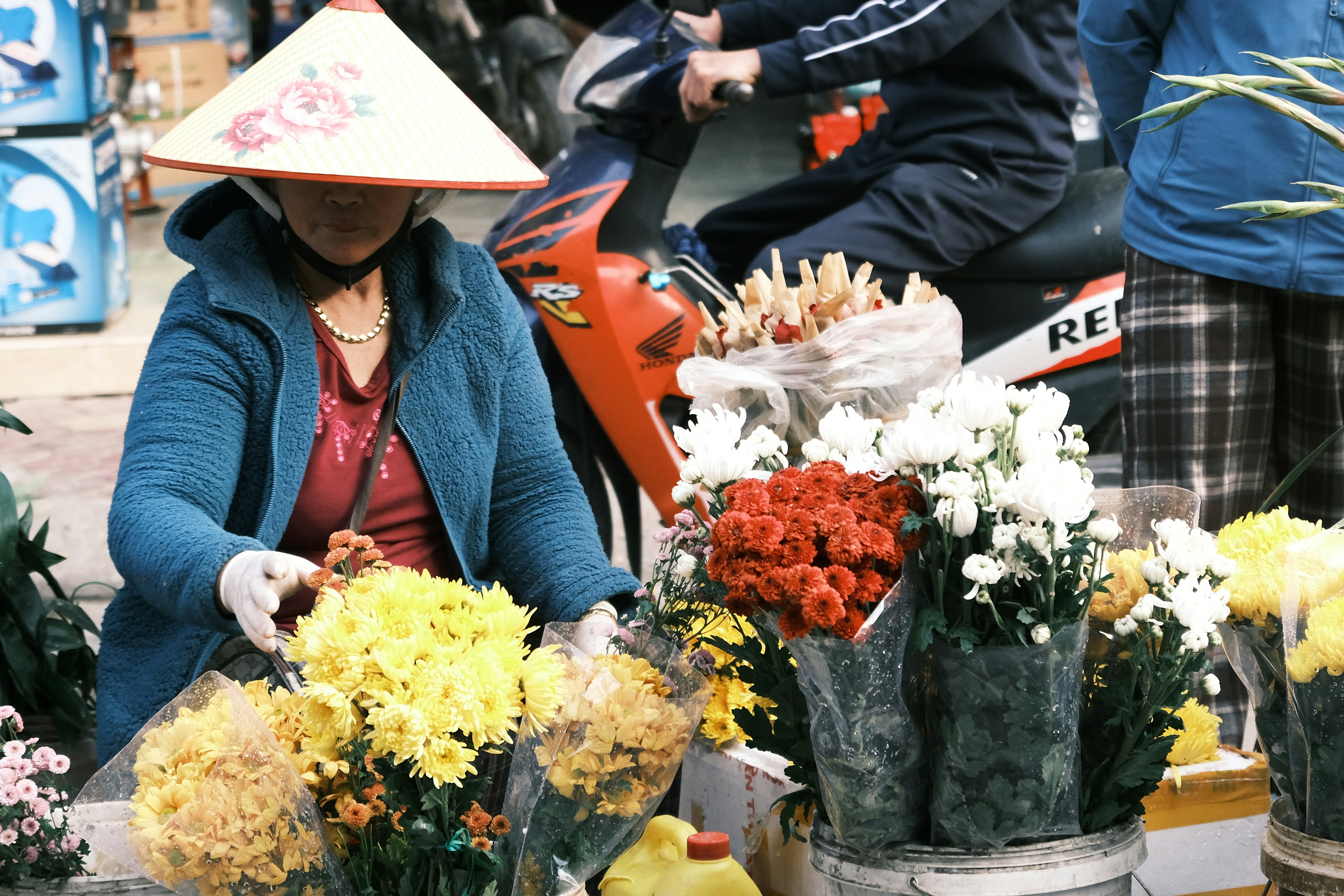 Vendor in traditional hat arranging colorful flowers at a bustling market stall.