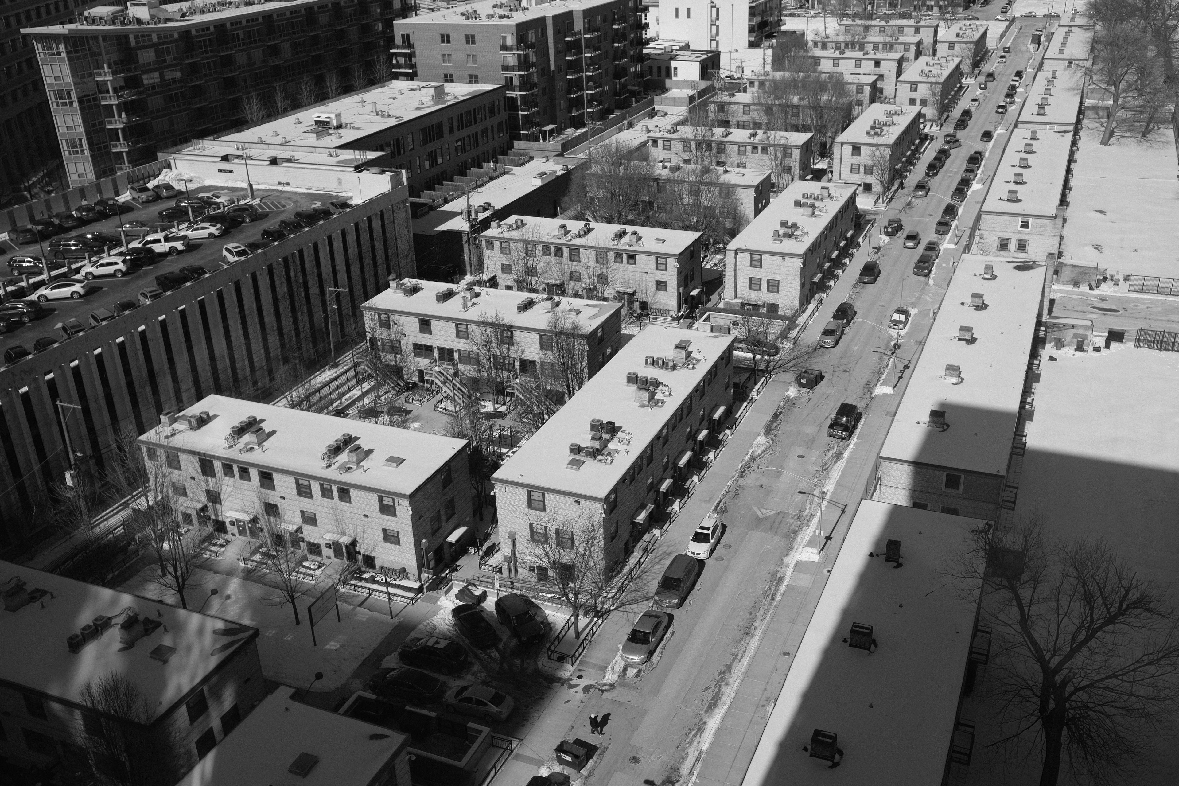 Snow-dusted city rooftops and streets create a geometric pattern under stark shadows.
