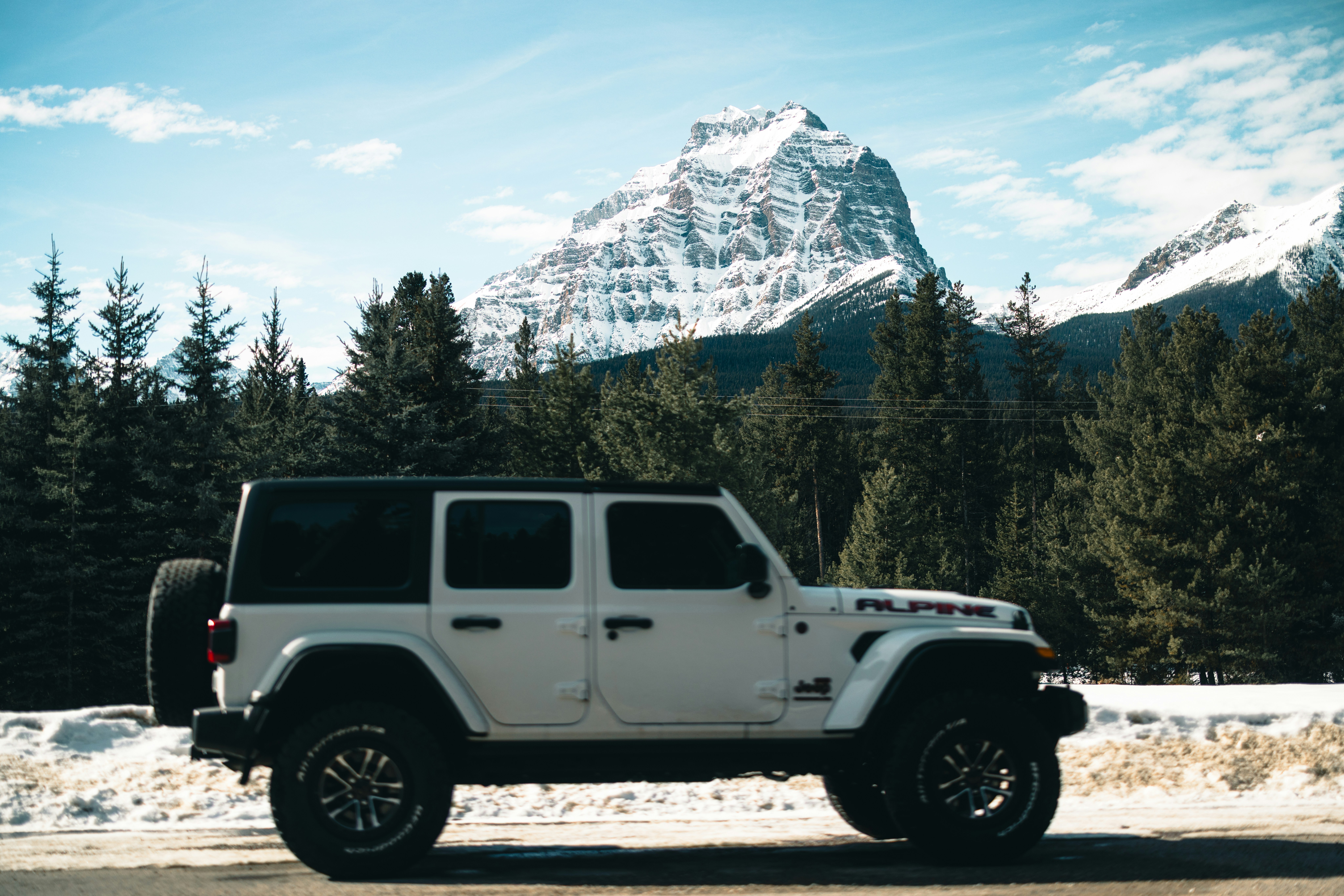 White SUV parked on snowy roadside with a majestic snow-capped mountain in the background.