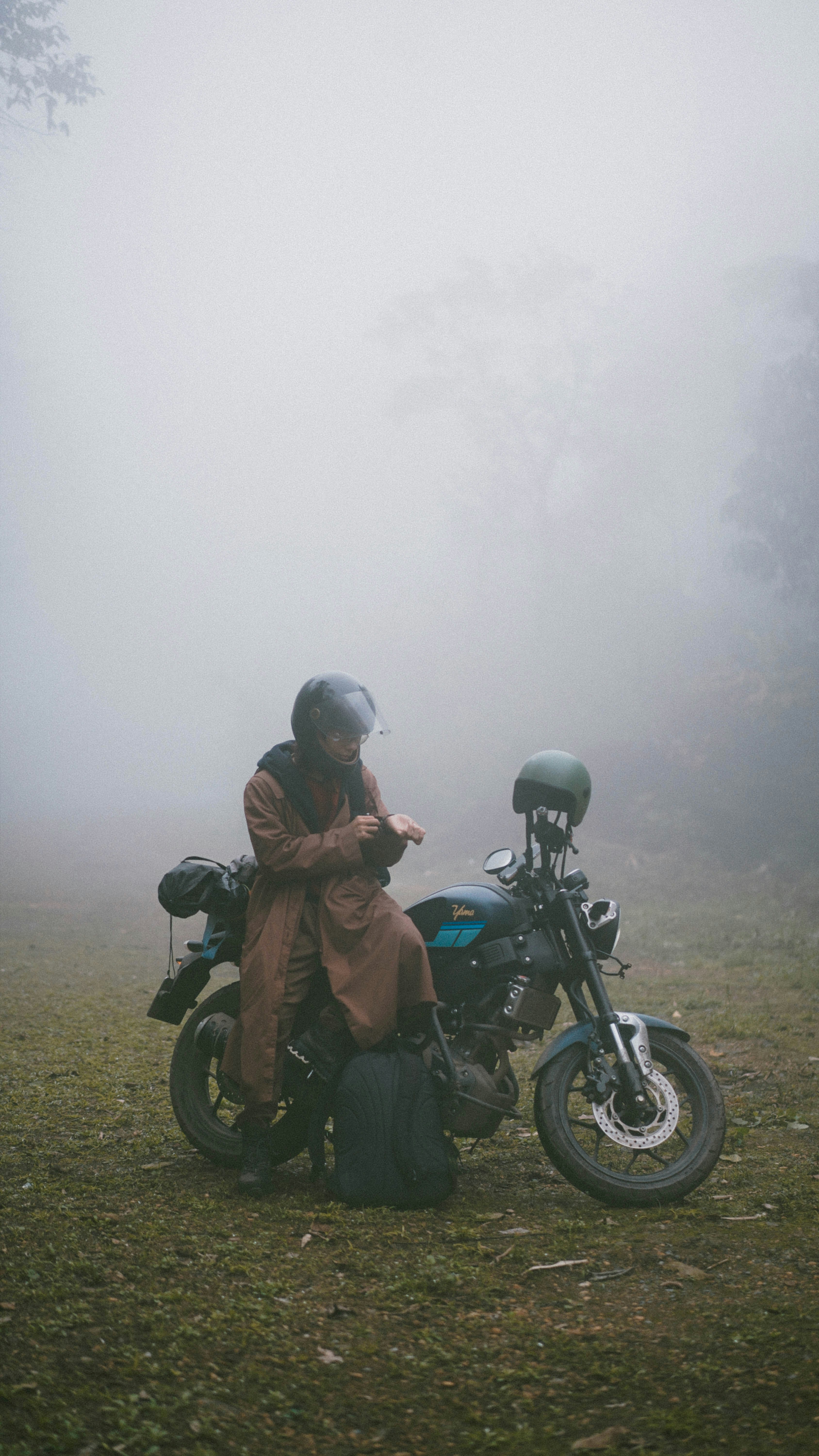 Fogbound on Two Wheels: A Rider Pauses by a Blue Motorcycle in Mist
