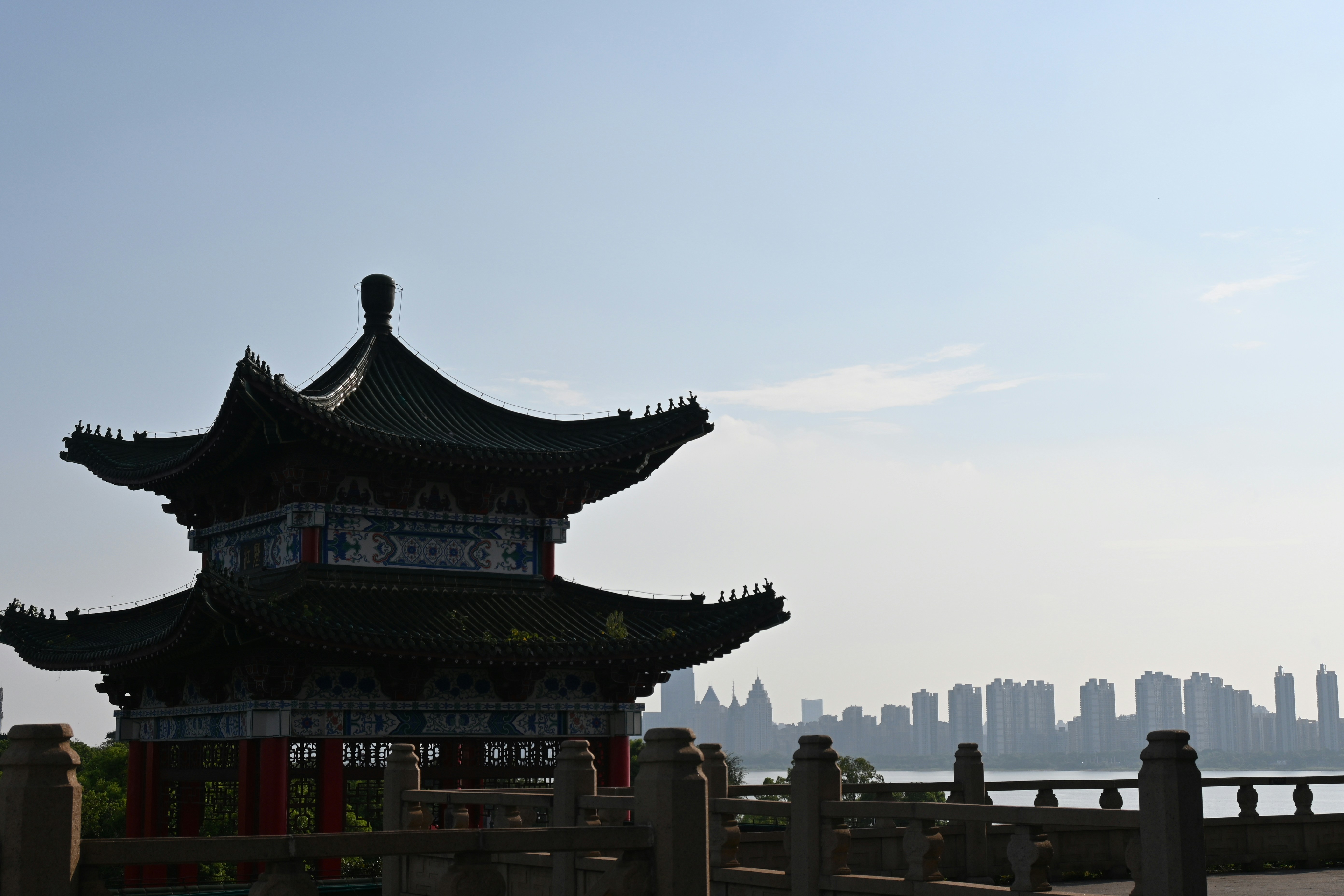 Traditional pavilion silhouetted against a city skyline under a clear blue sky.