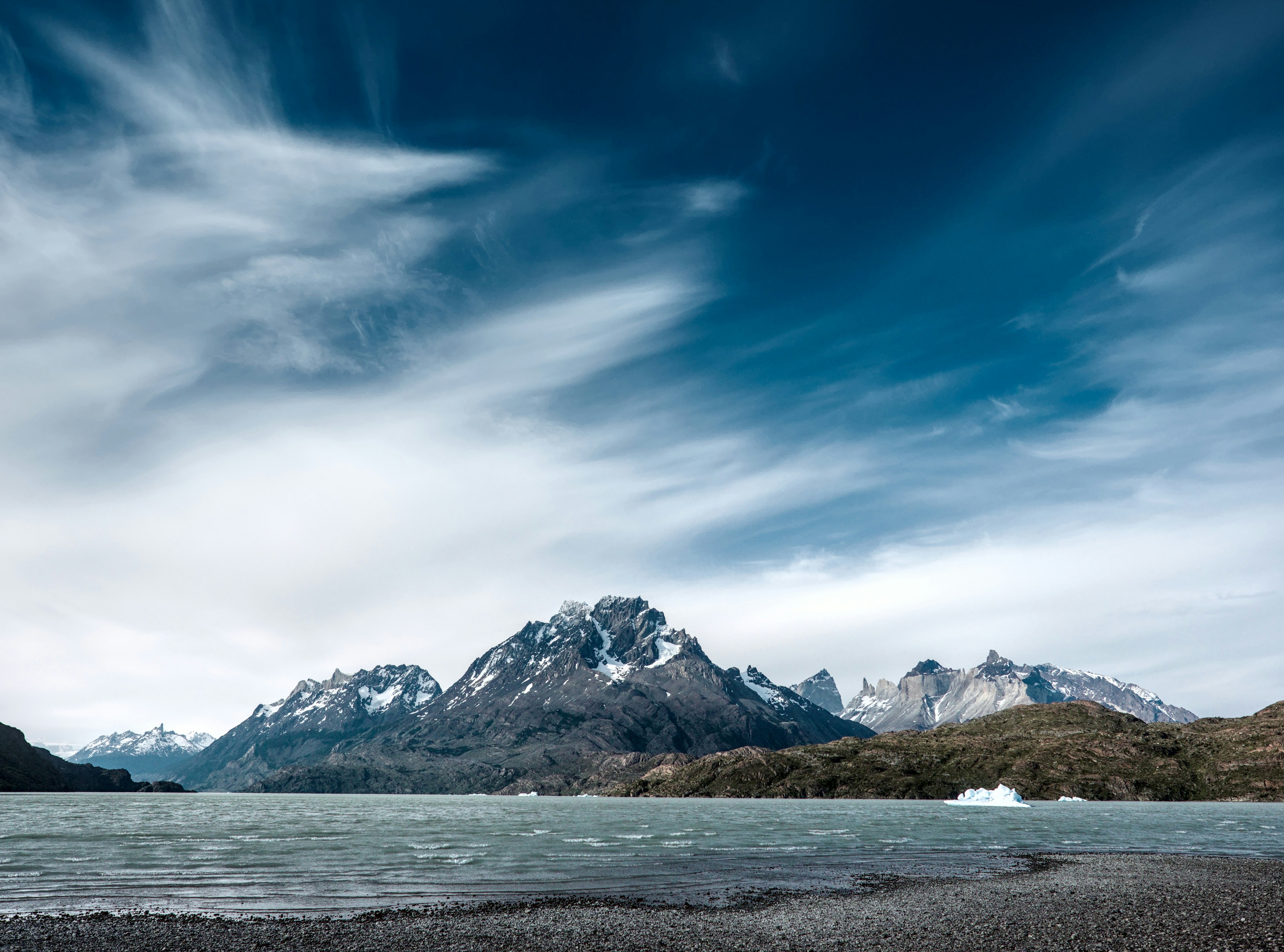Snow-capped mountains reflected in the tranquil waters of Lago Grey under a vast, dynamic sky.