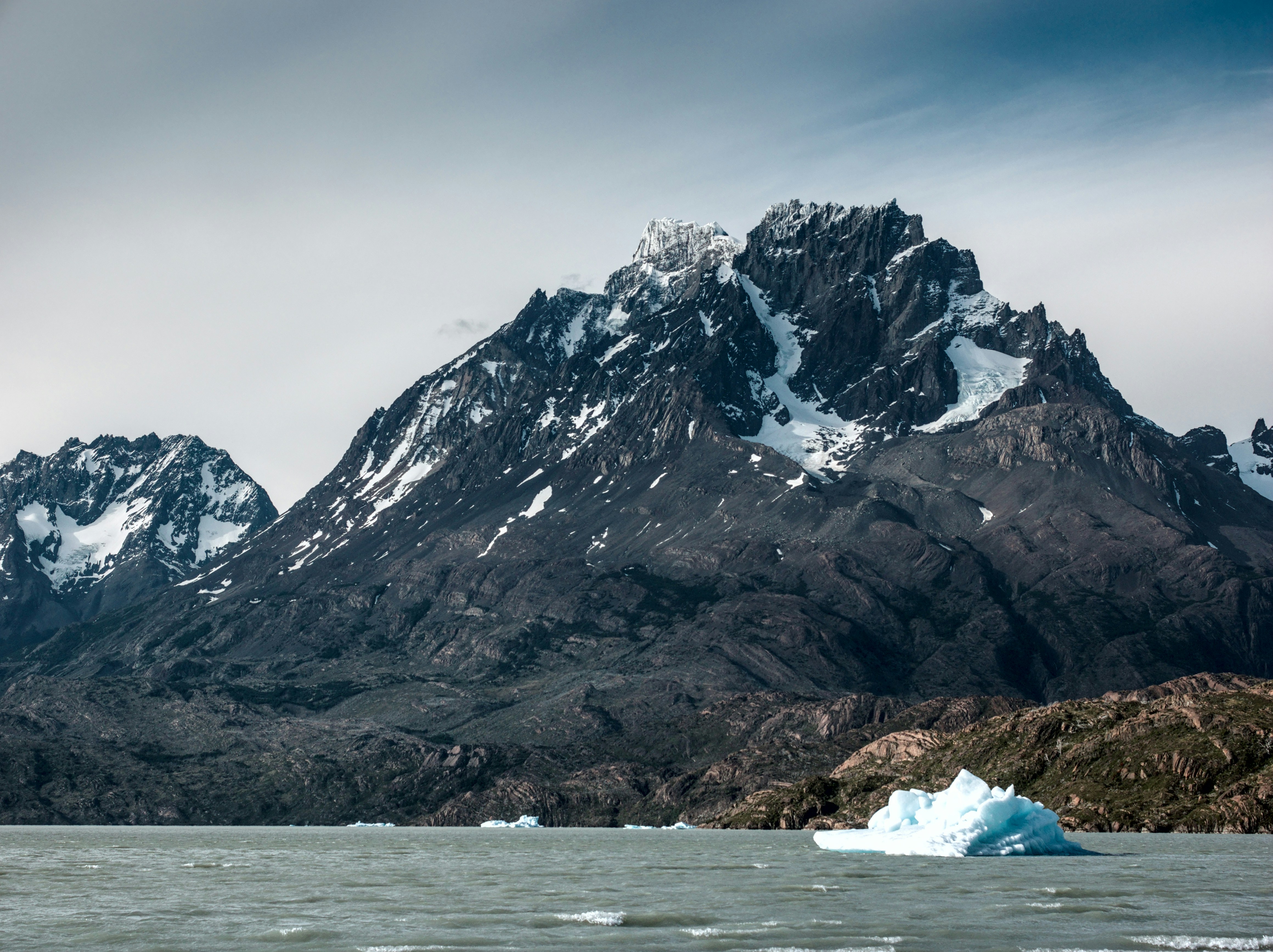 Snow-capped mountains tower above a serene lake with floating icebergs in Torres del Paine, Chile.