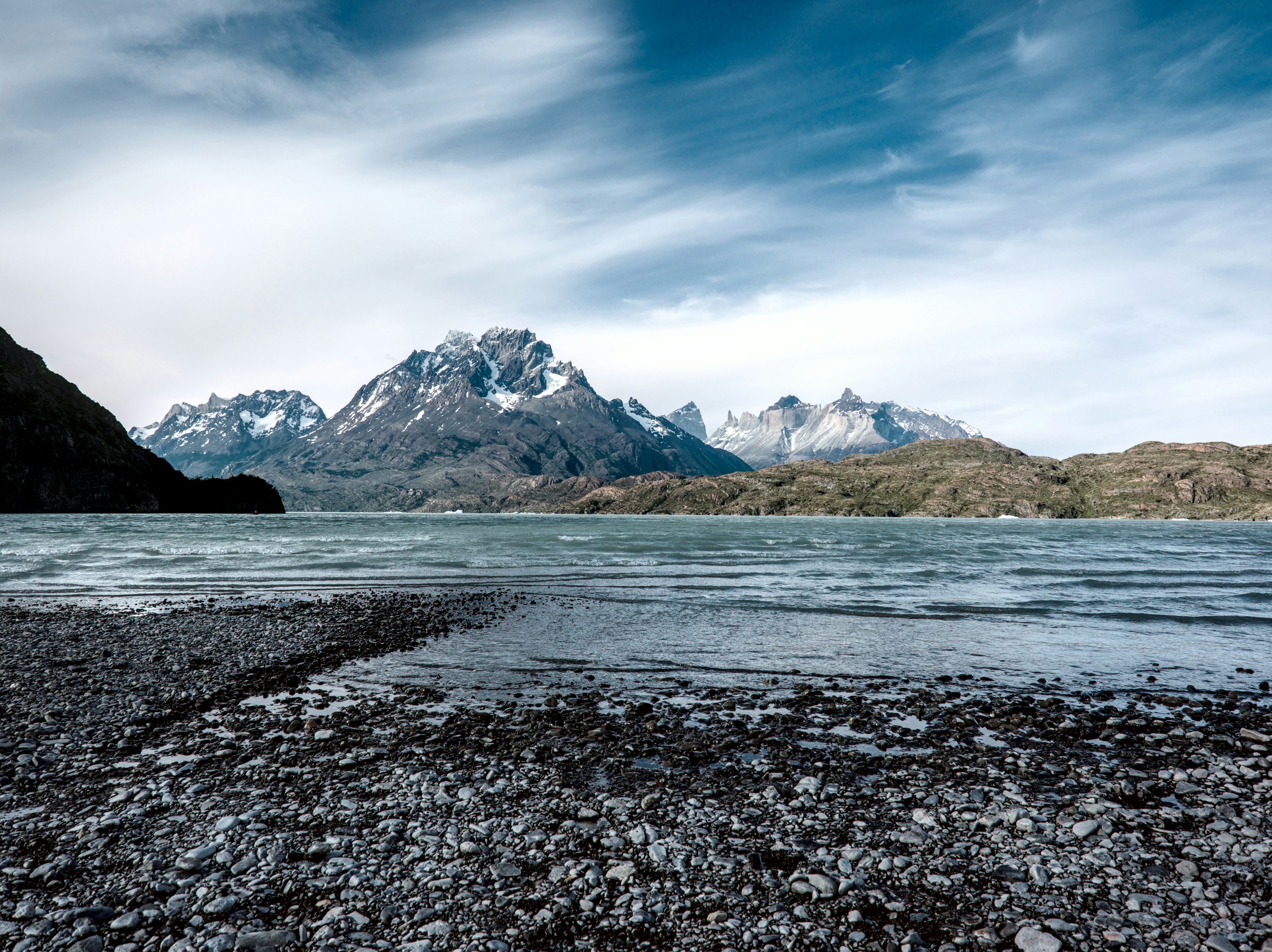 Snow-capped mountains reflected in the tranquil waters of Lago Grey under a vast, cloudy sky.