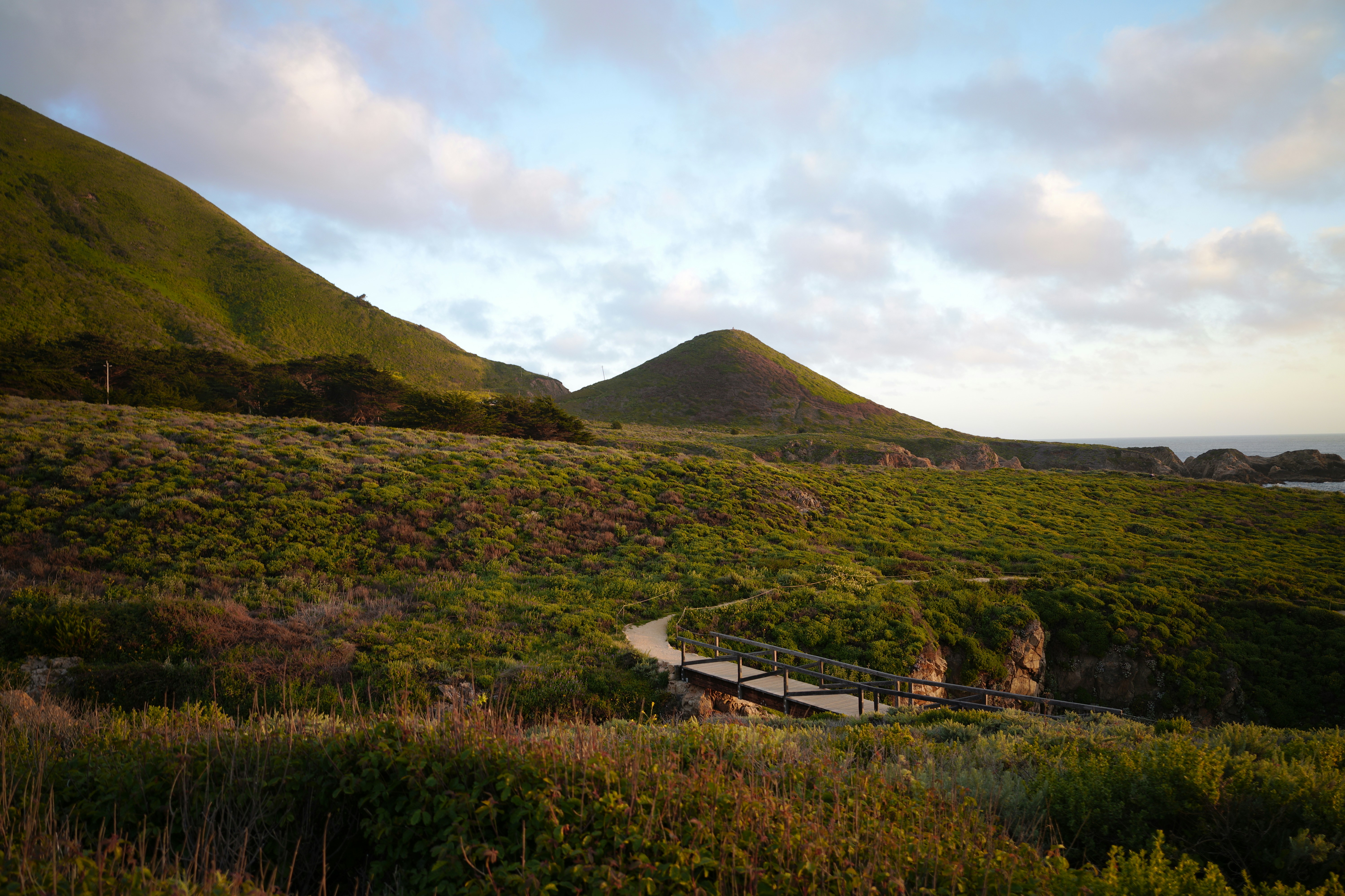 Lush green hills with a winding pathway under a partly cloudy sky.