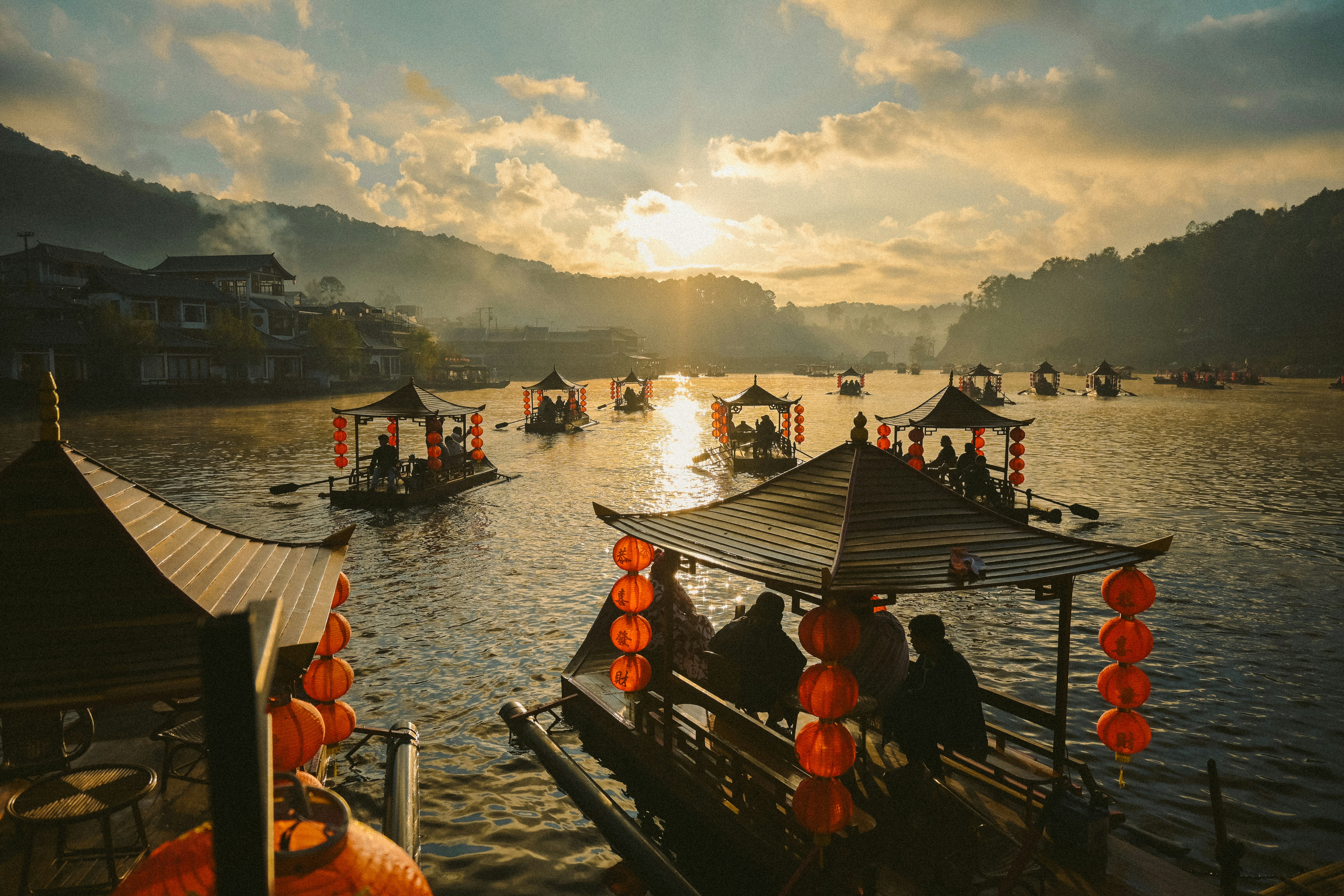 Wooden boats adorned with red lanterns drift on a serene lake at sunset.