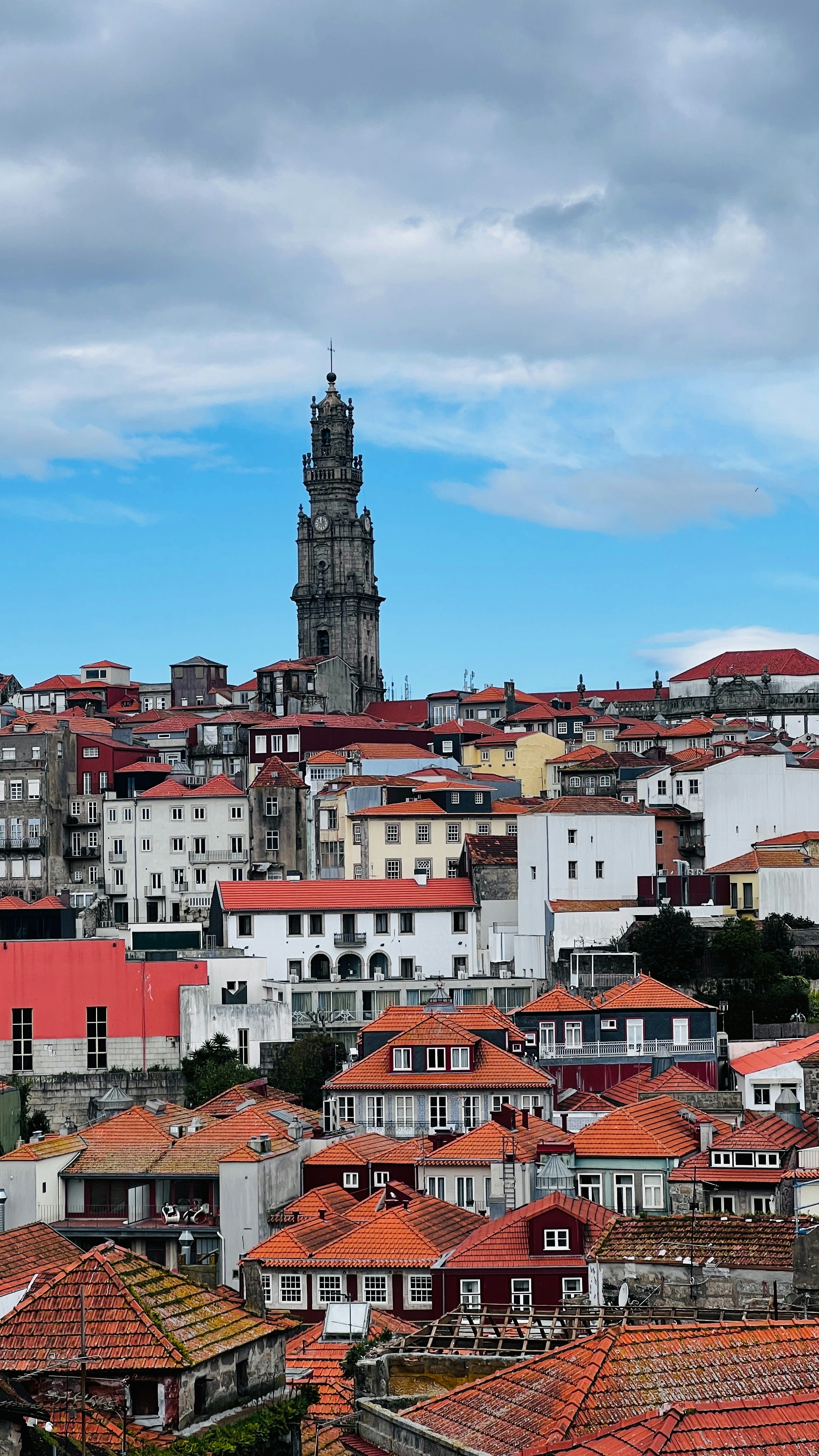 Historic tower rises above a patchwork of colorful rooftops in a vibrant urban landscape. The scene captures the essence of city life against a dramatic sky.