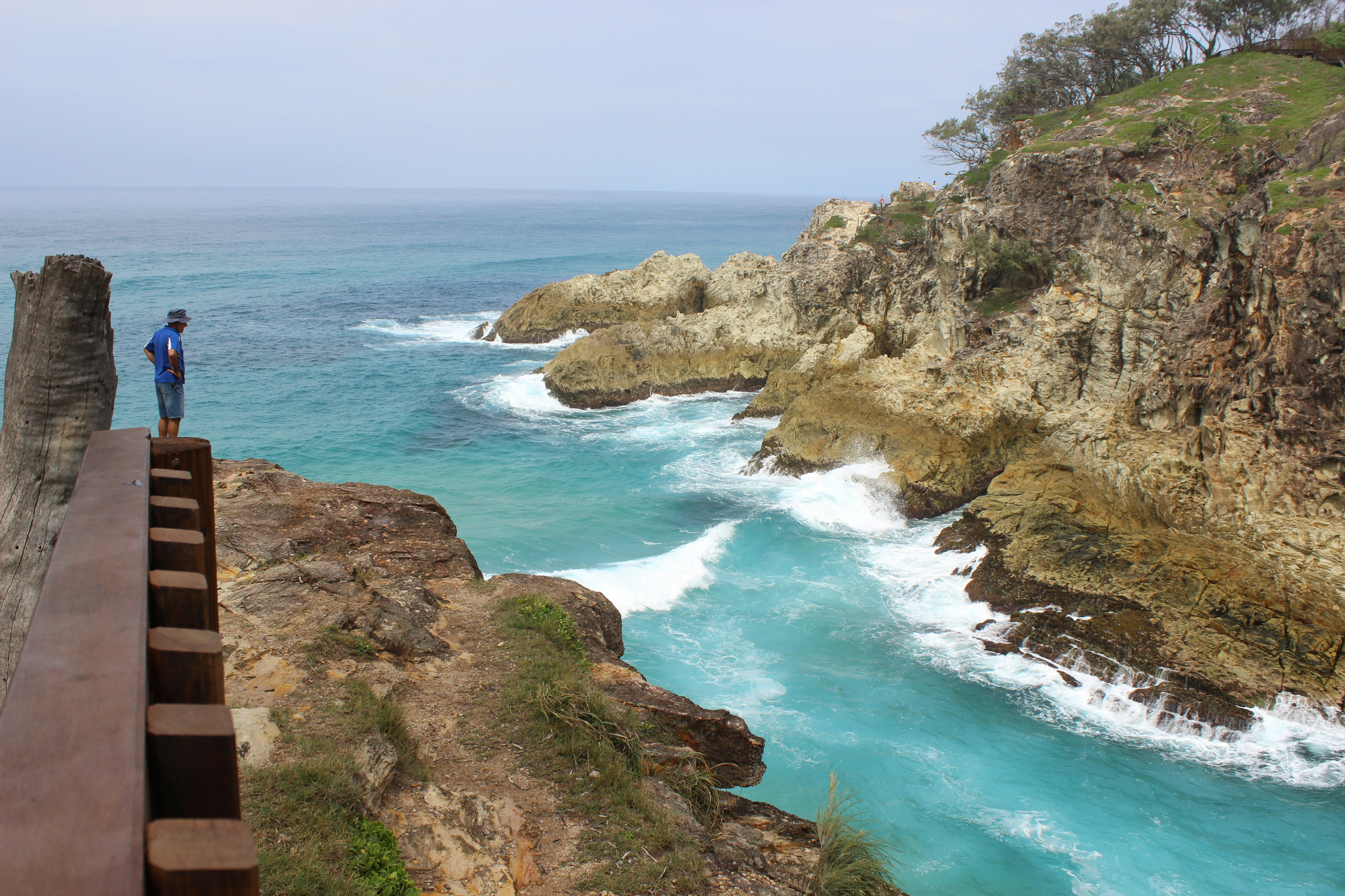 Person standing on a rocky cliff overlooking turquoise waves crashing against the shore.