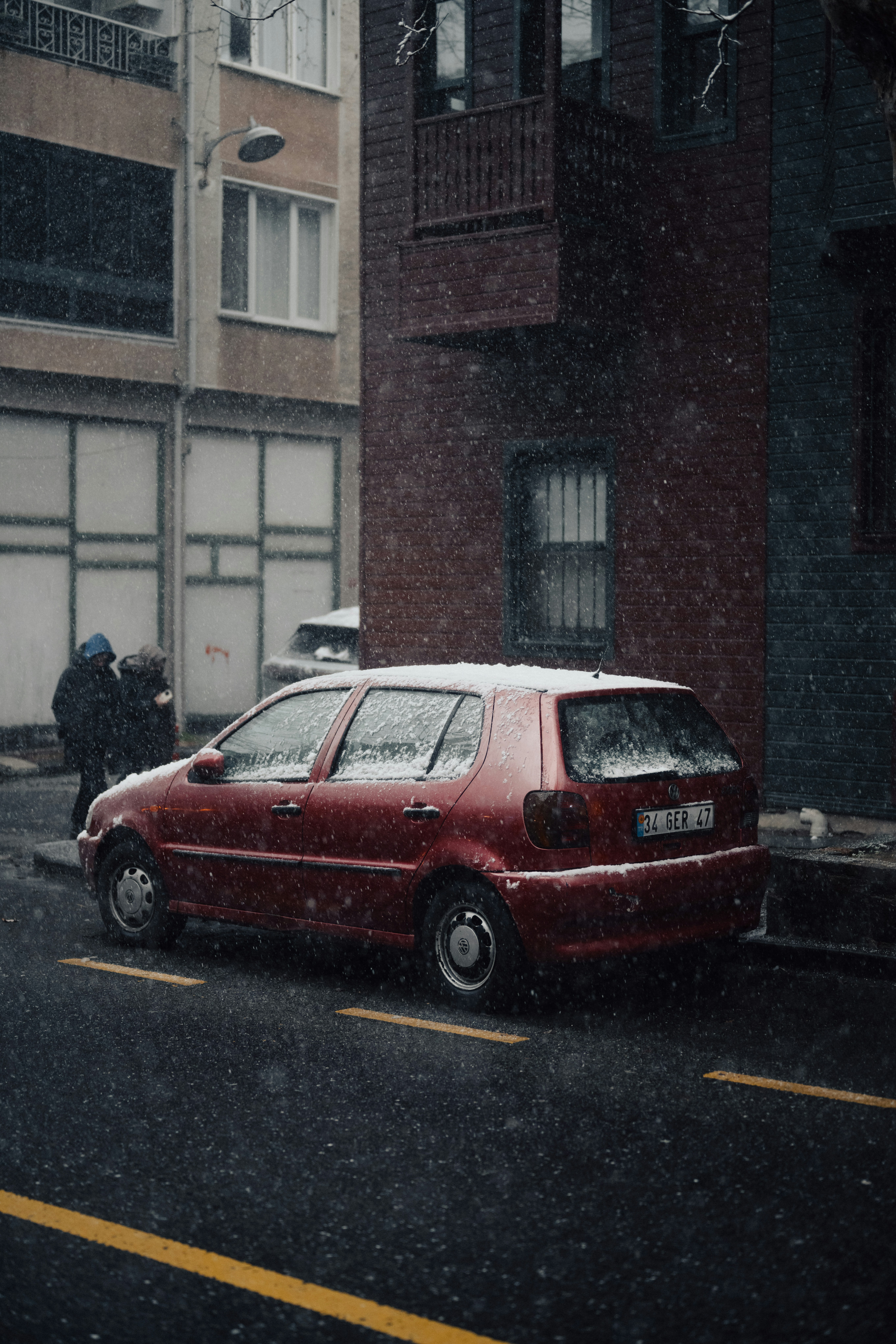 Crimson Hatchback Beneath Falling Snow on a Quiet Urban Street