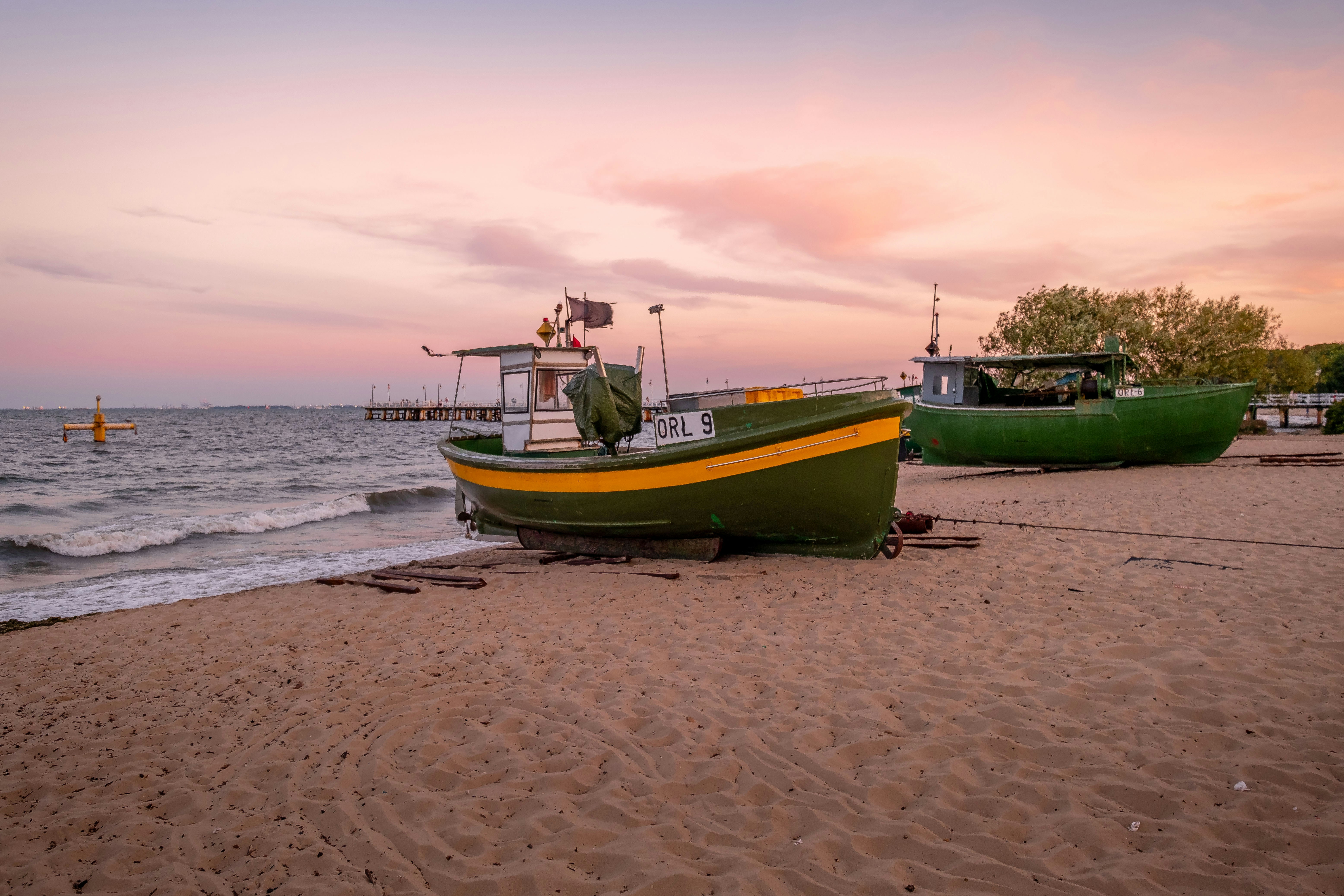 Colorful fishing boats rest on a sandy beach at sunset, with gentle waves lapping the shore.