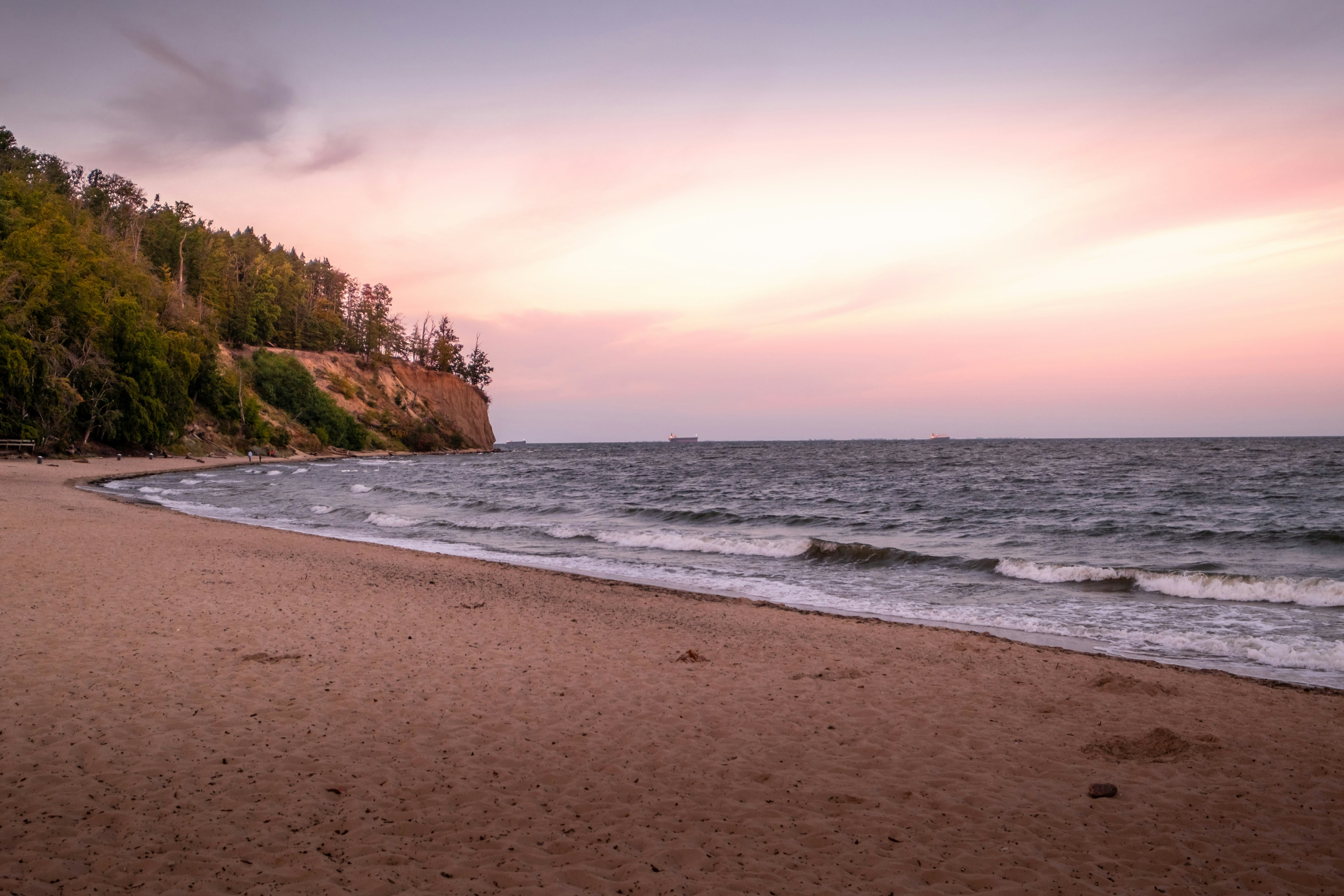 Beach with gentle waves under a pastel-colored sunset sky.