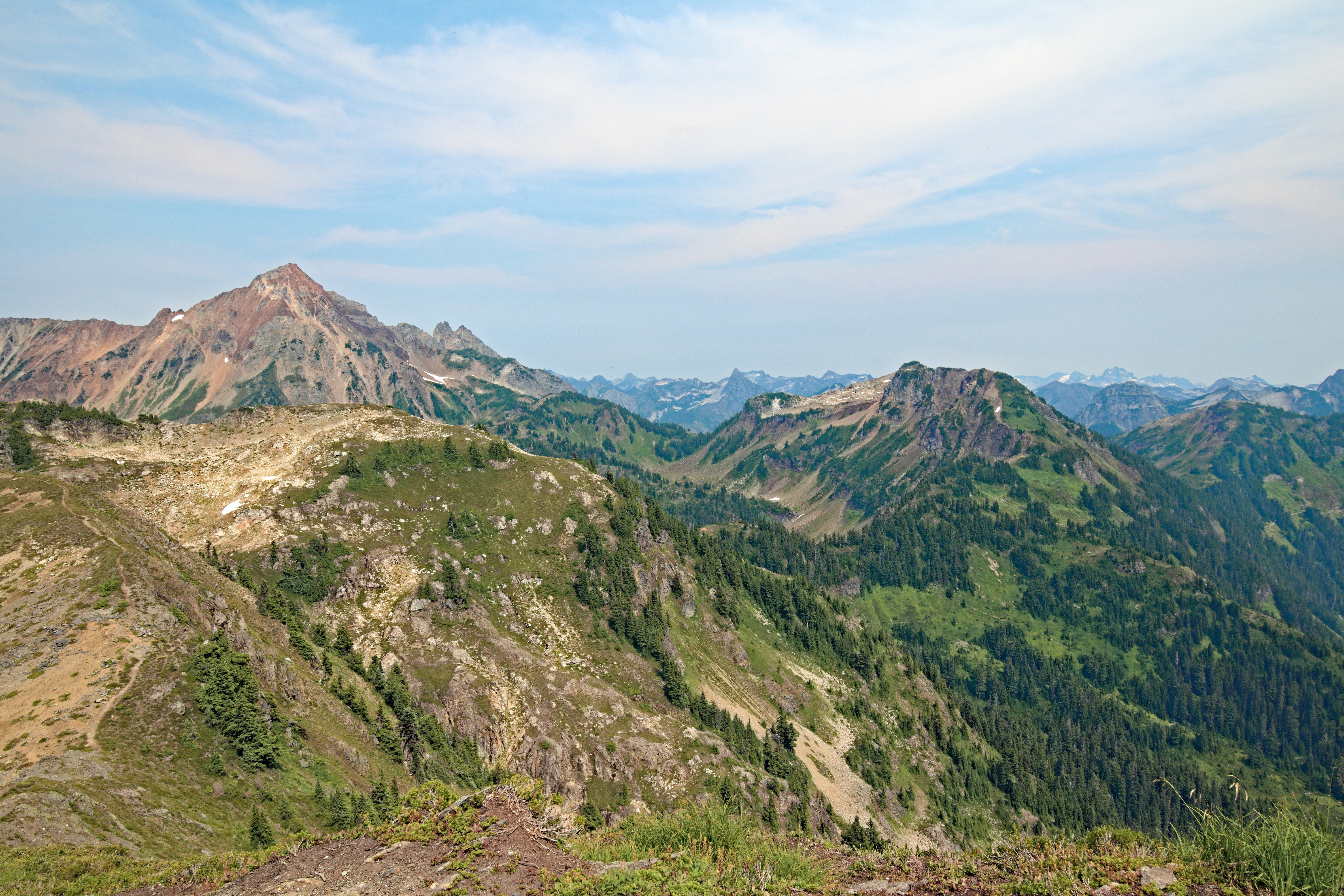Lush green ridges and distant rocky peaks under a softly clouded sky.