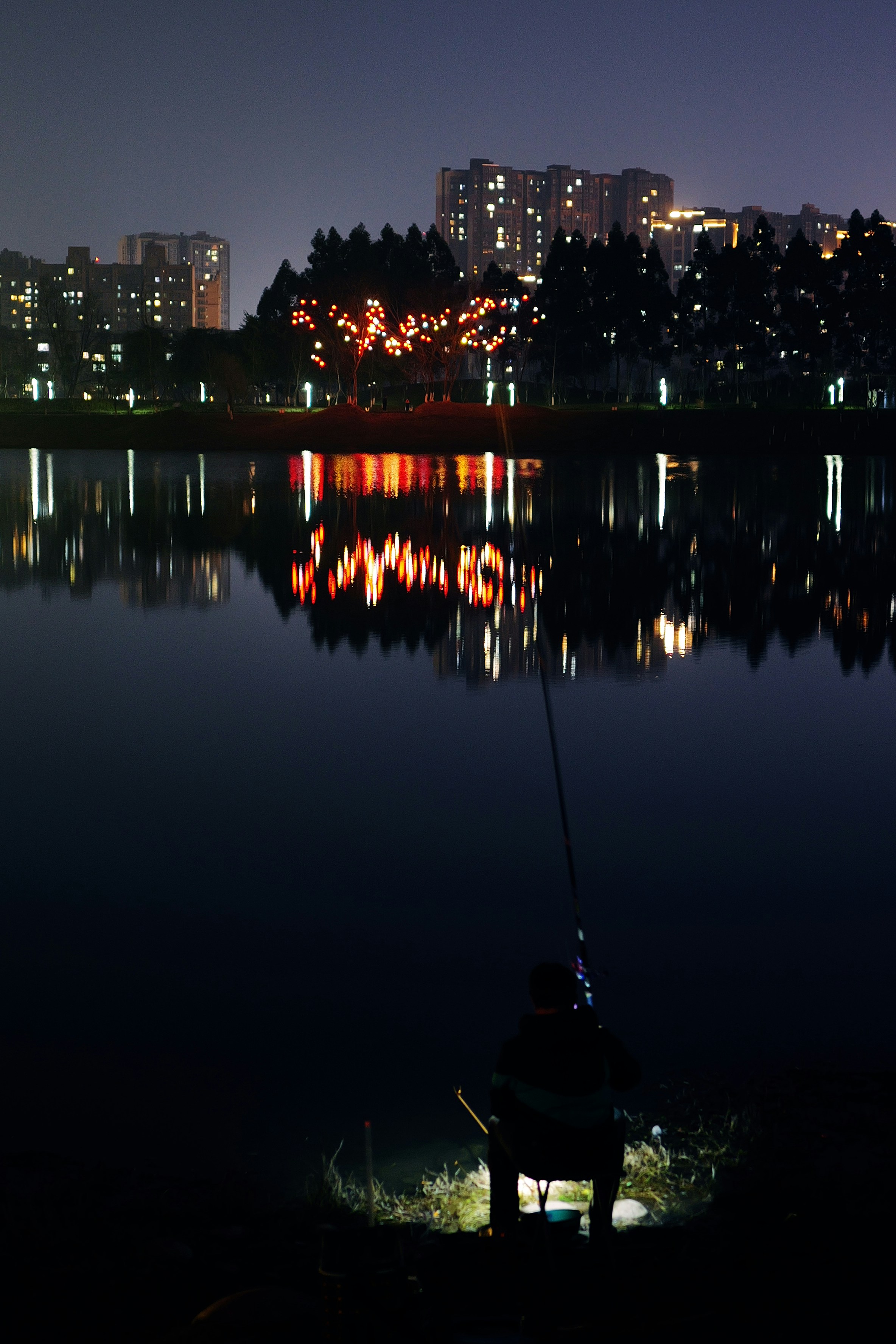 Midnight Cast: A lone angler by the lake beneath city glow