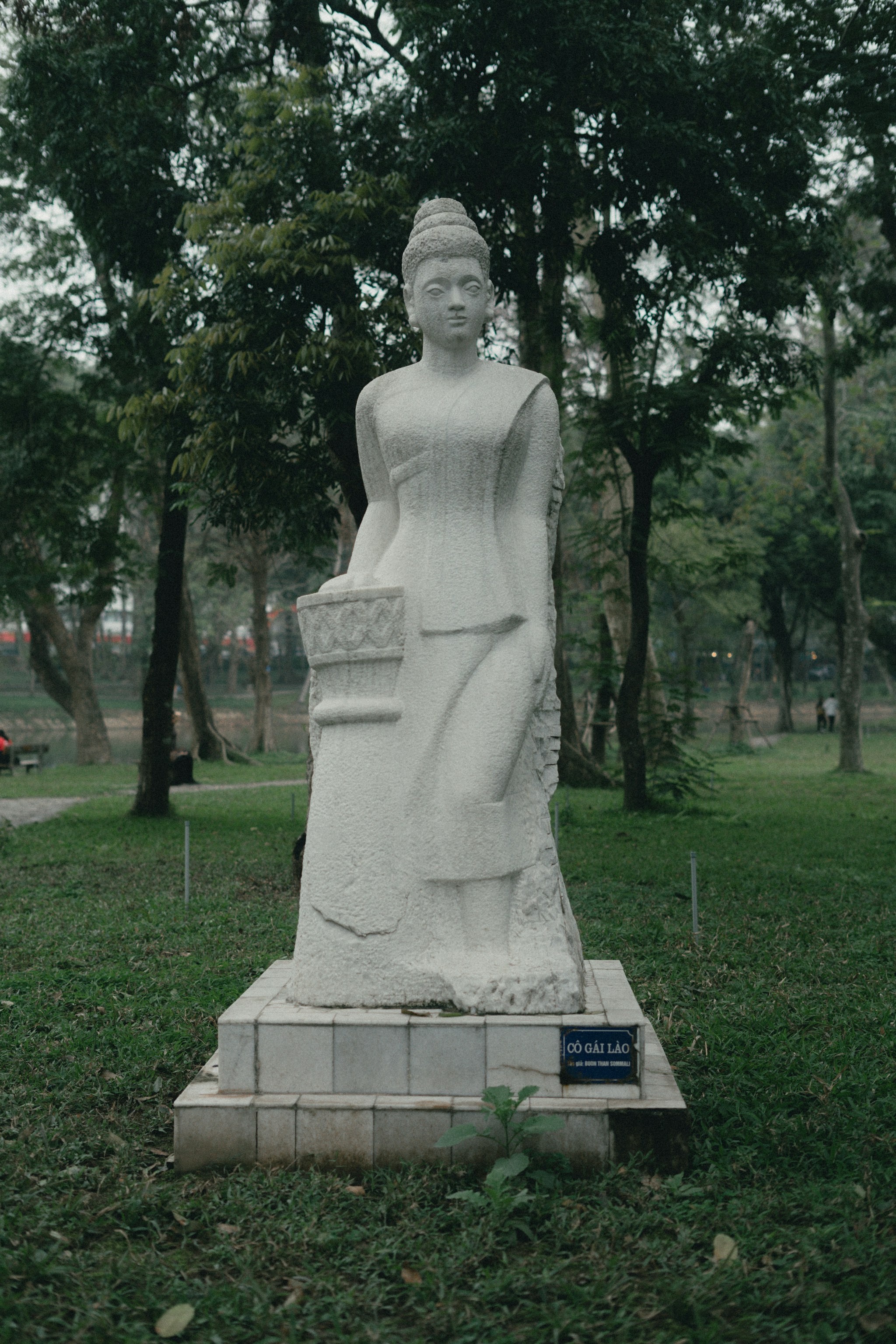 Verdant Reverie: A Stone Buddha Standing Amid Park Treescape