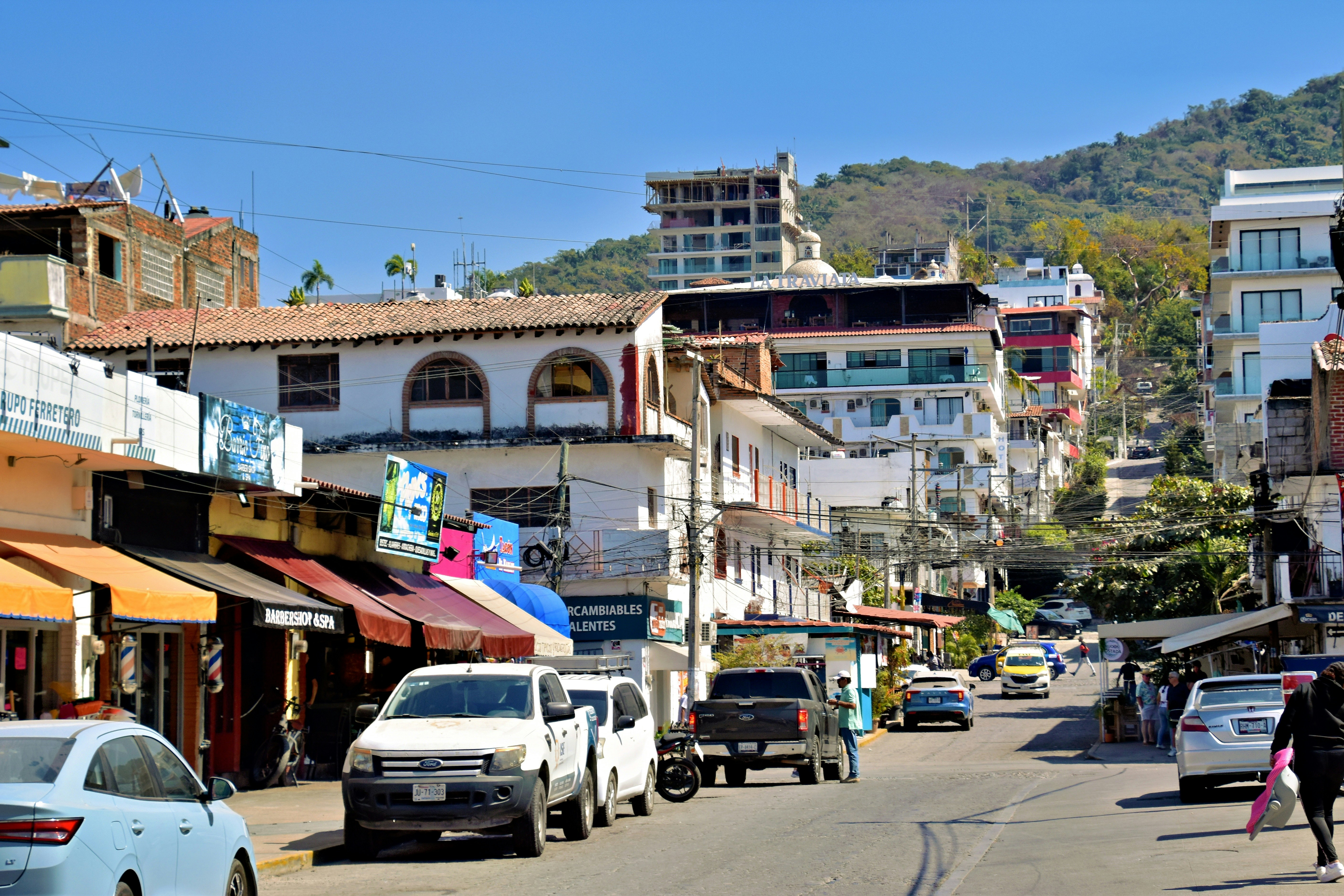 Busy urban street lined with colorful buildings and parked vehicles under a clear blue sky.