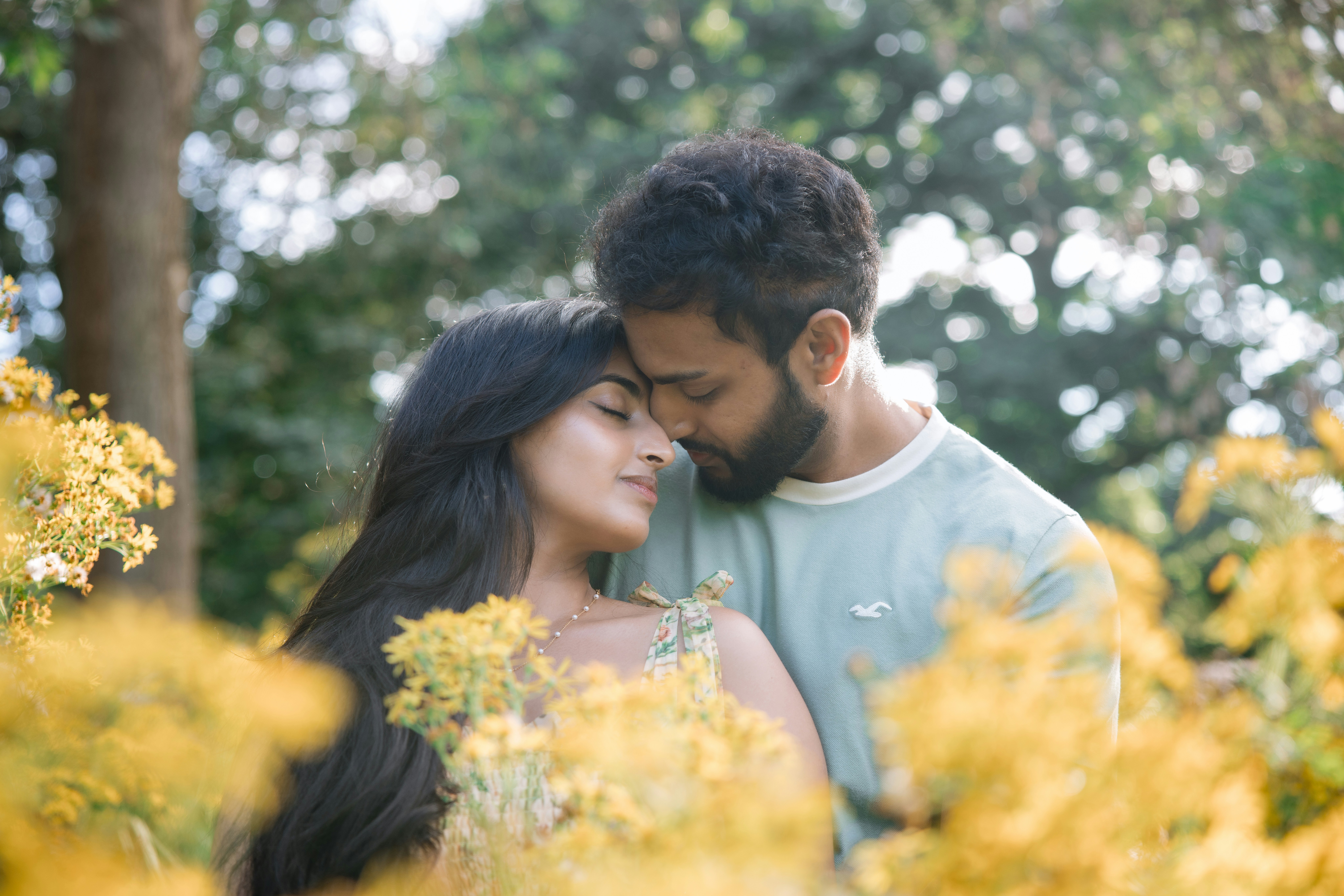 Couple embraces tenderly amidst vibrant yellow wildflowers in a sunlit forest.