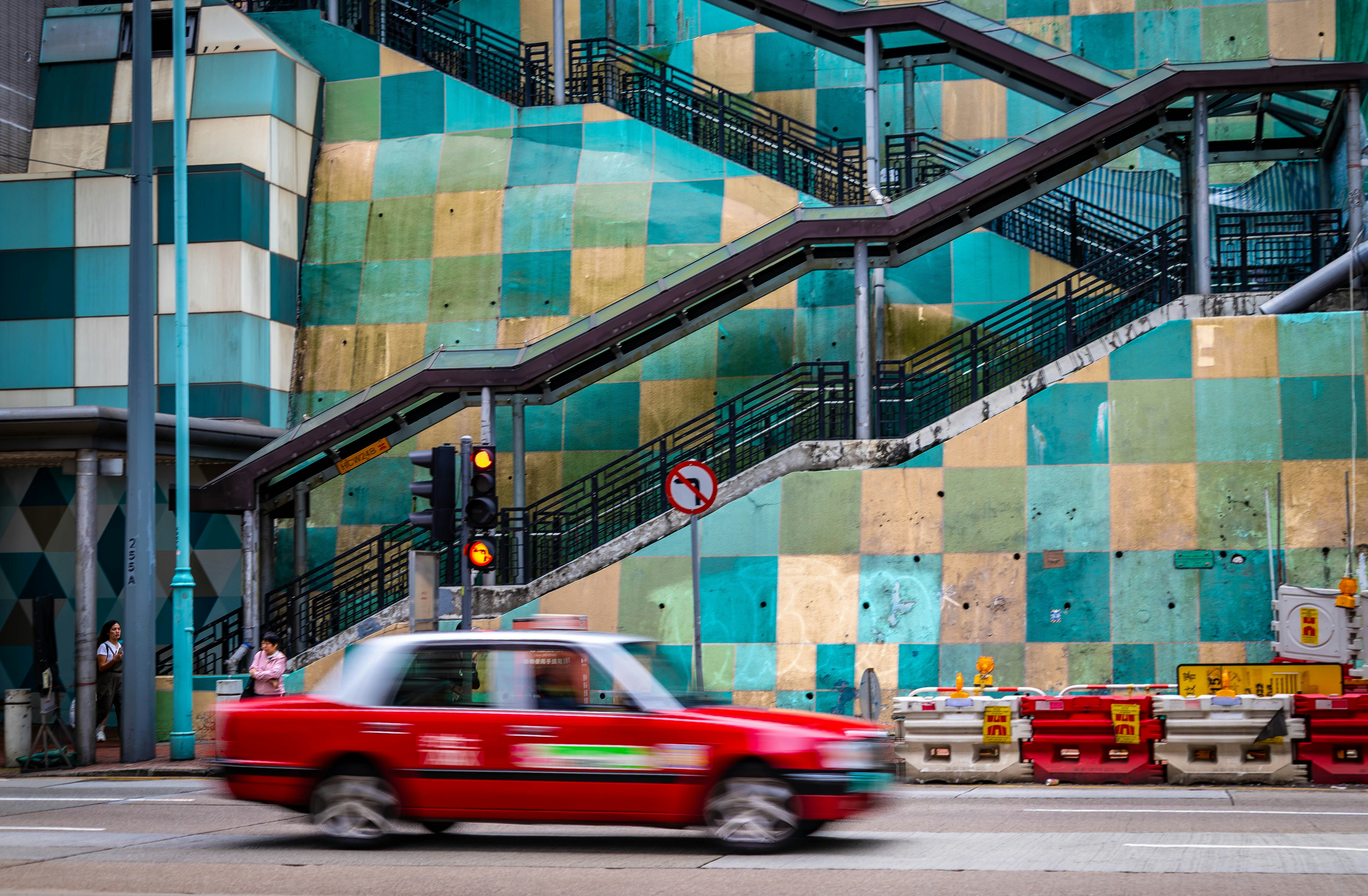 Crimson Taxi in Motion Across a Patchwork Facade