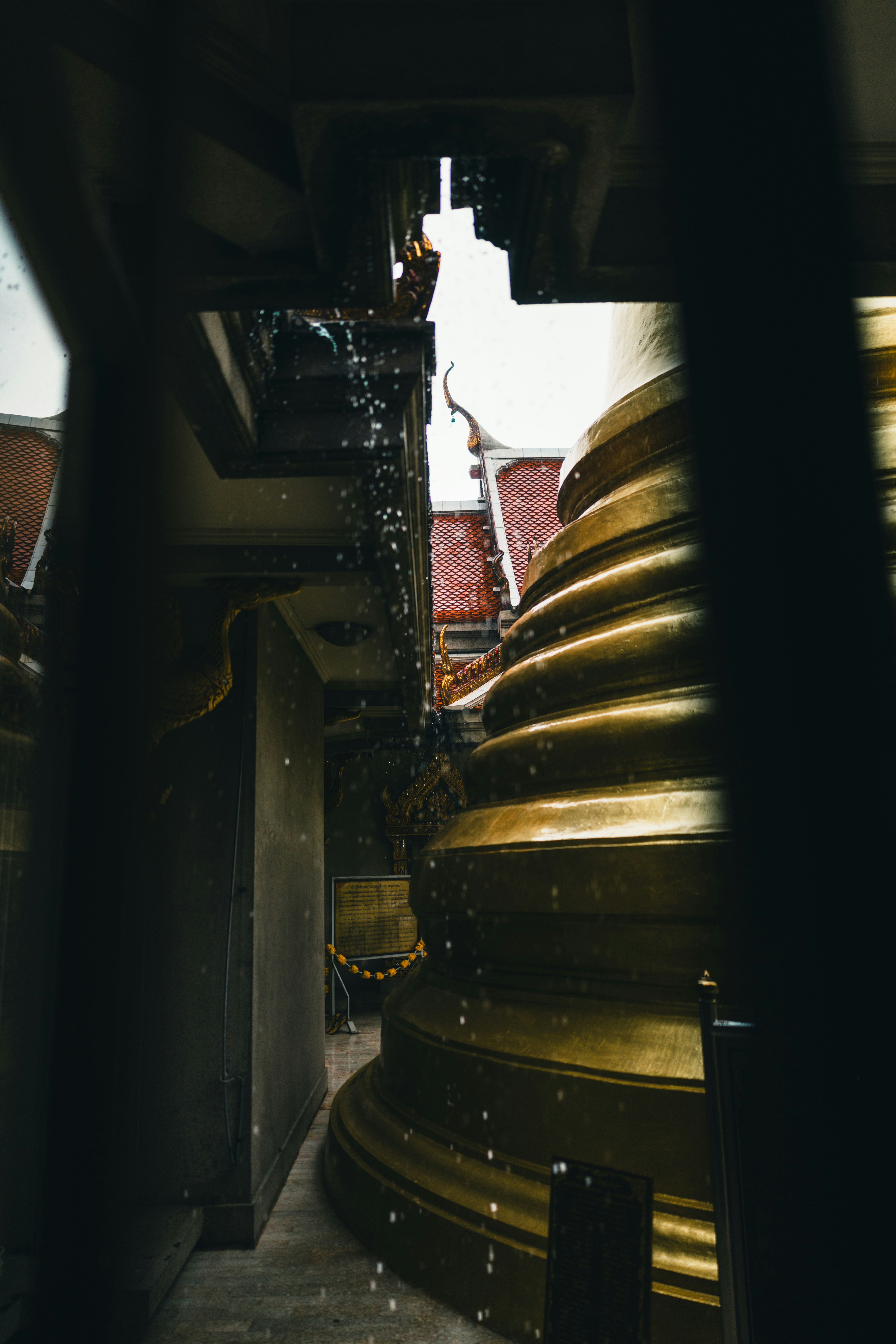 Golden stupa partially visible through a narrow opening, framed by architectural details and droplets of water, hinting at a serene temple atmosphere.