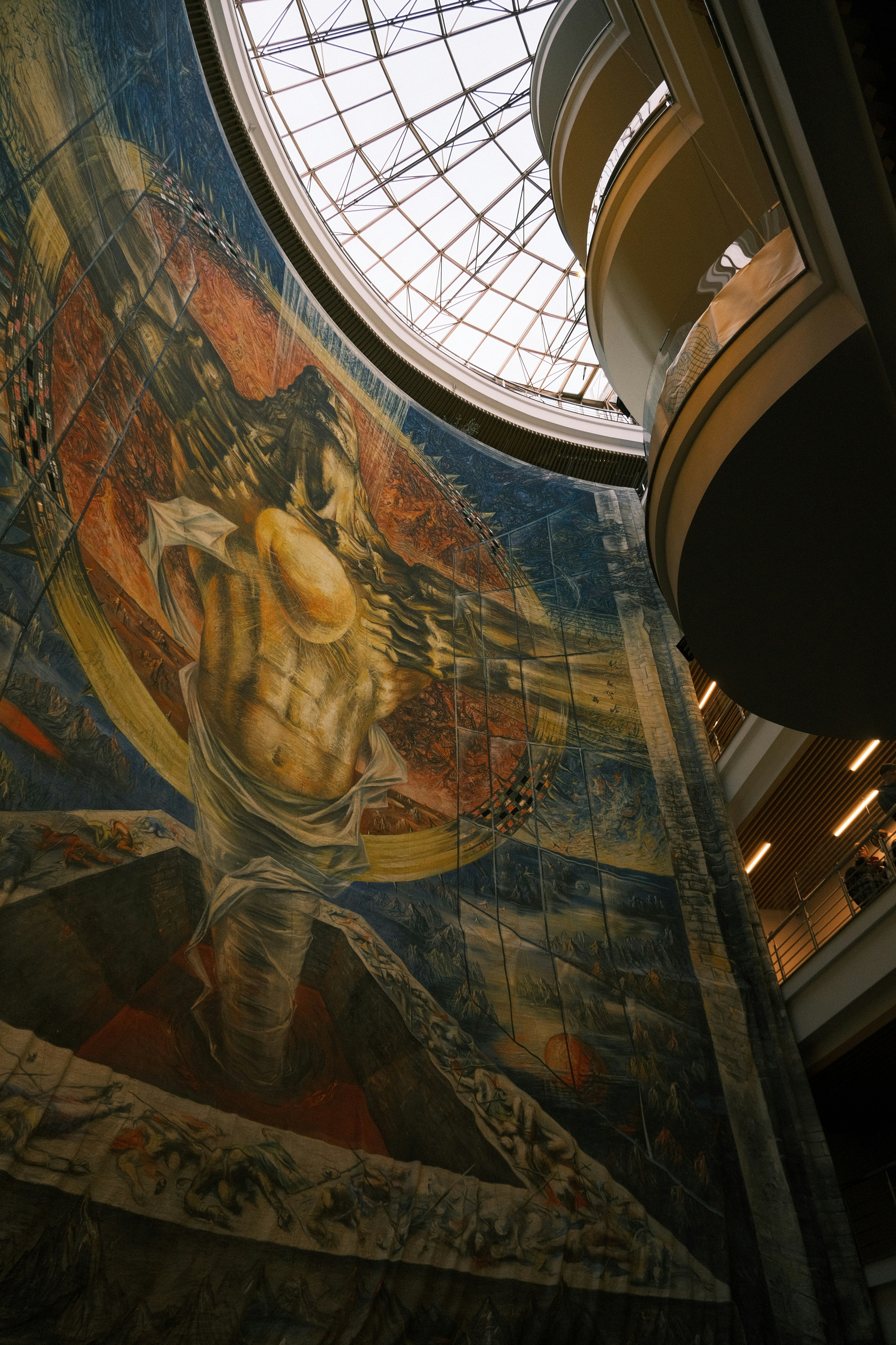 Large, colorful theatrical curtain beneath a curved, glass ceiling in a modern building.