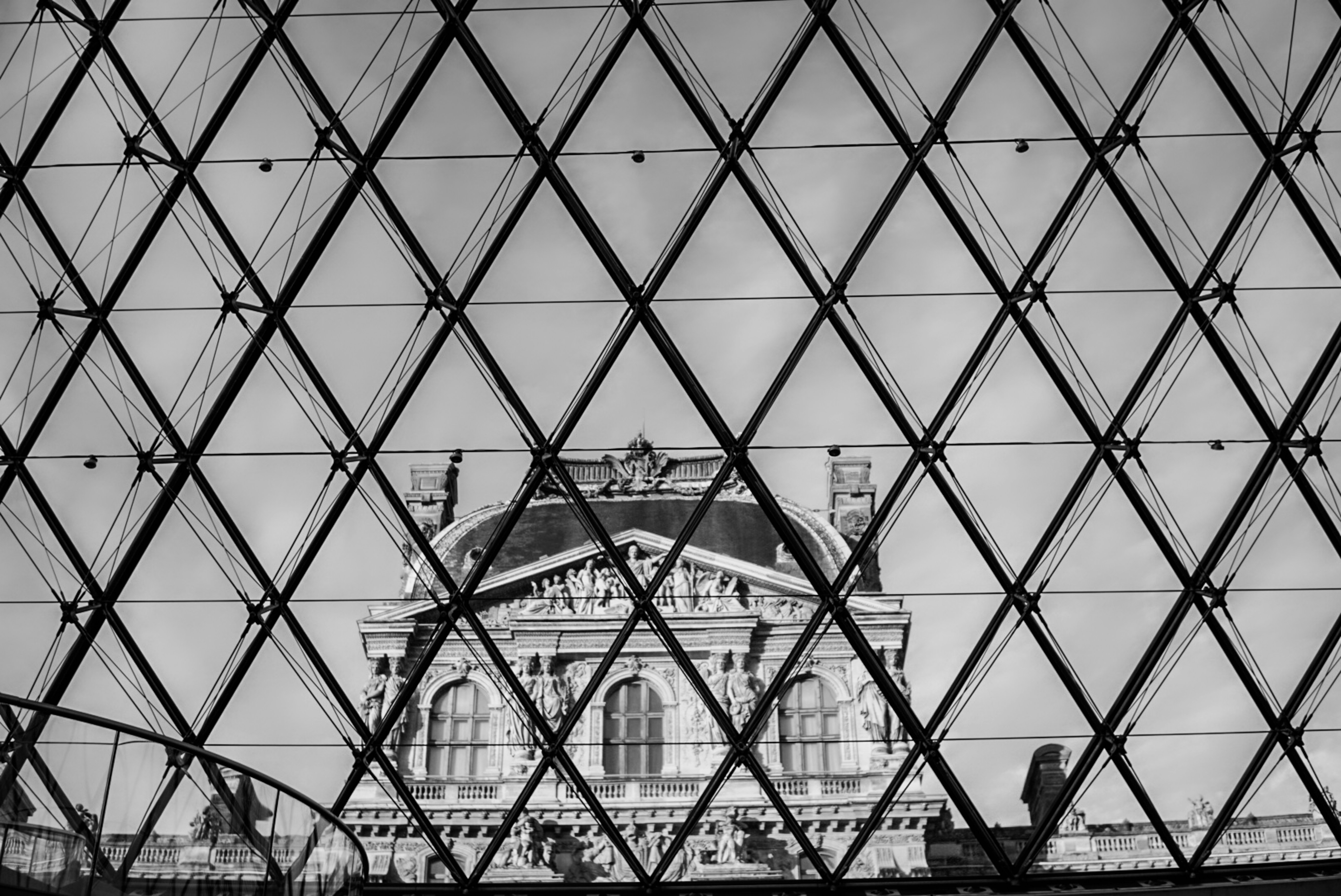 Historic Louvre facade framed by geometric glass lattice.