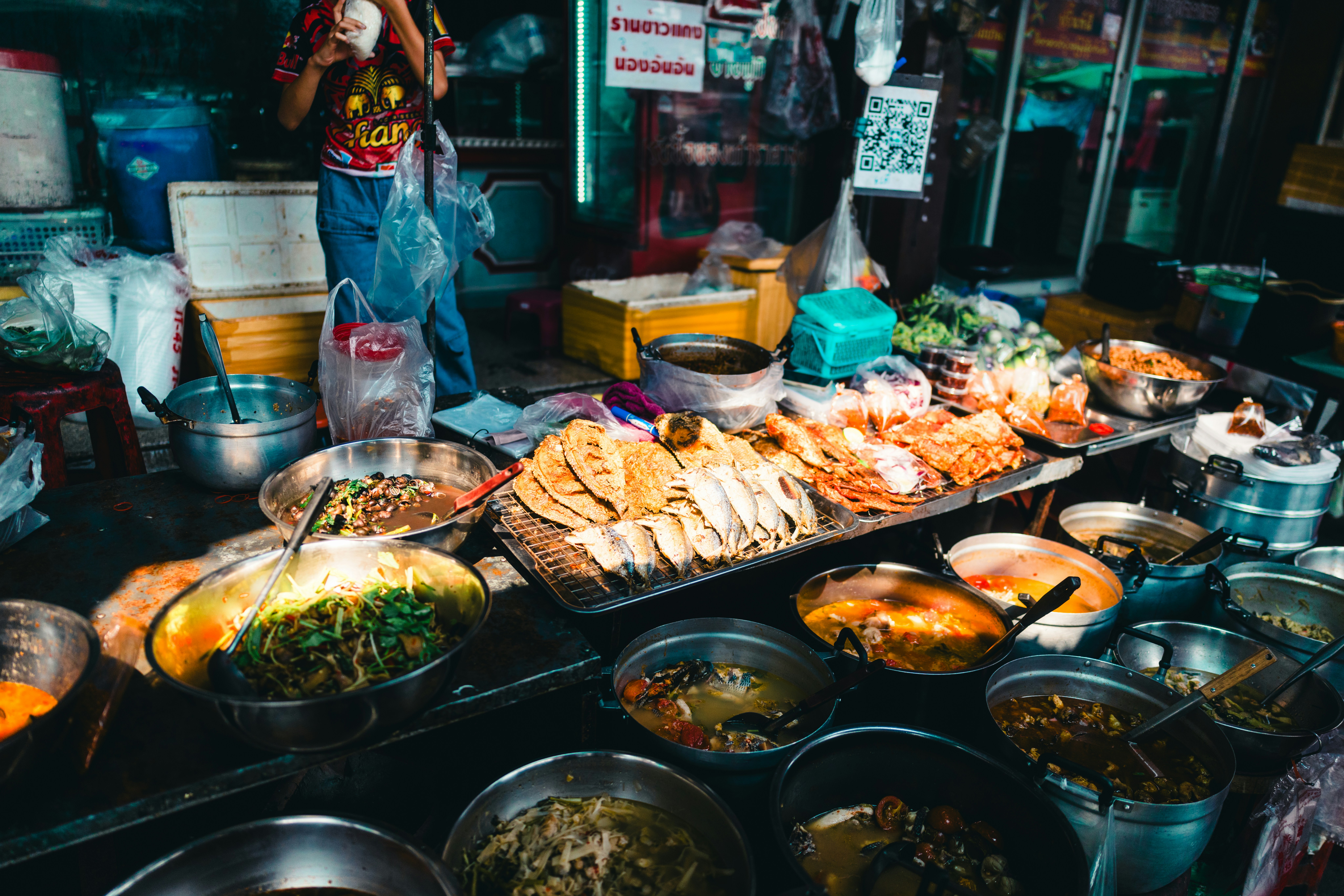 Vibrant street food stall in Bangkok with an array of colorful dishes displayed under bright lights.