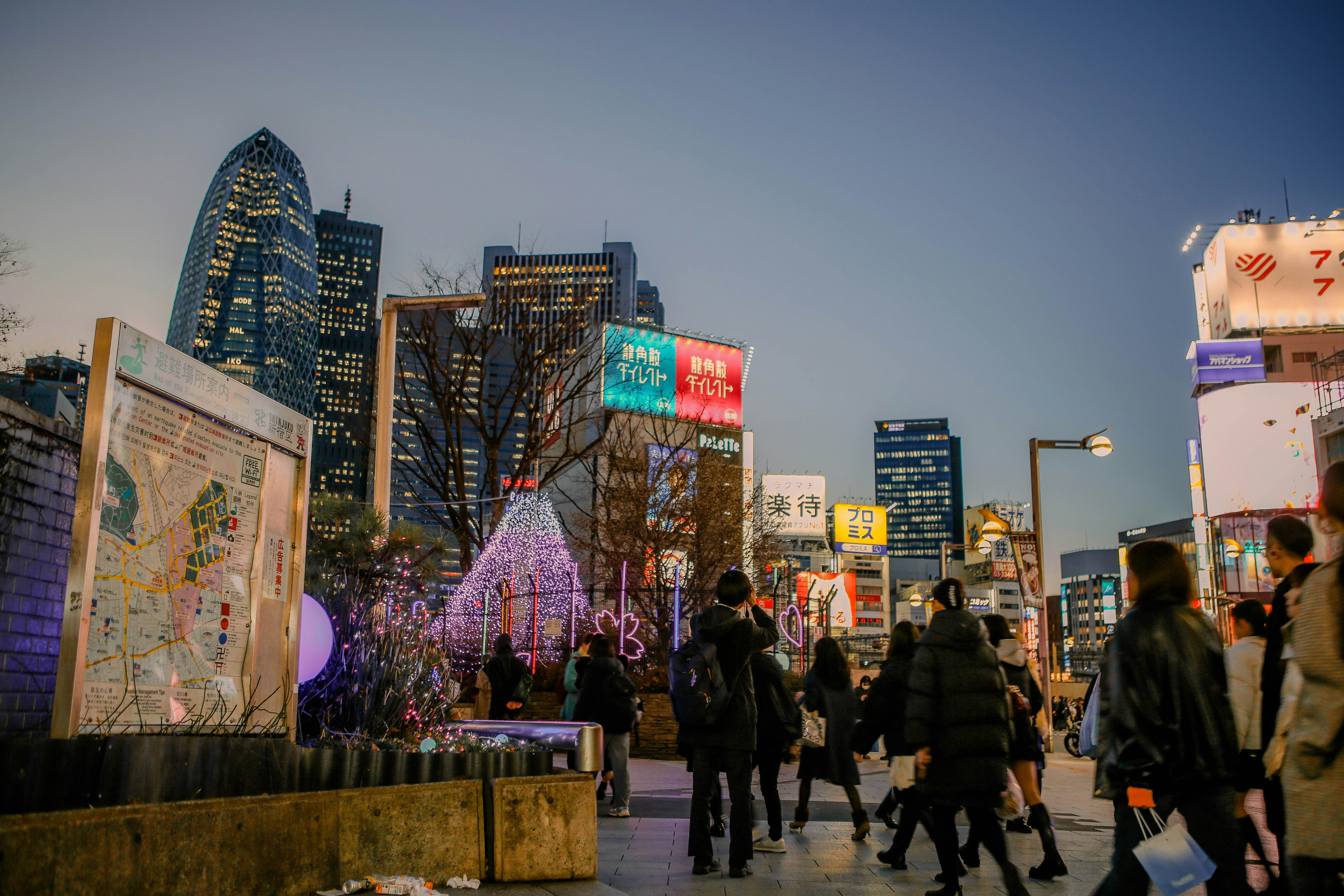 Bustling crowd in a vibrant Tokyo street with illuminated decorations and skyscrapers at dusk.