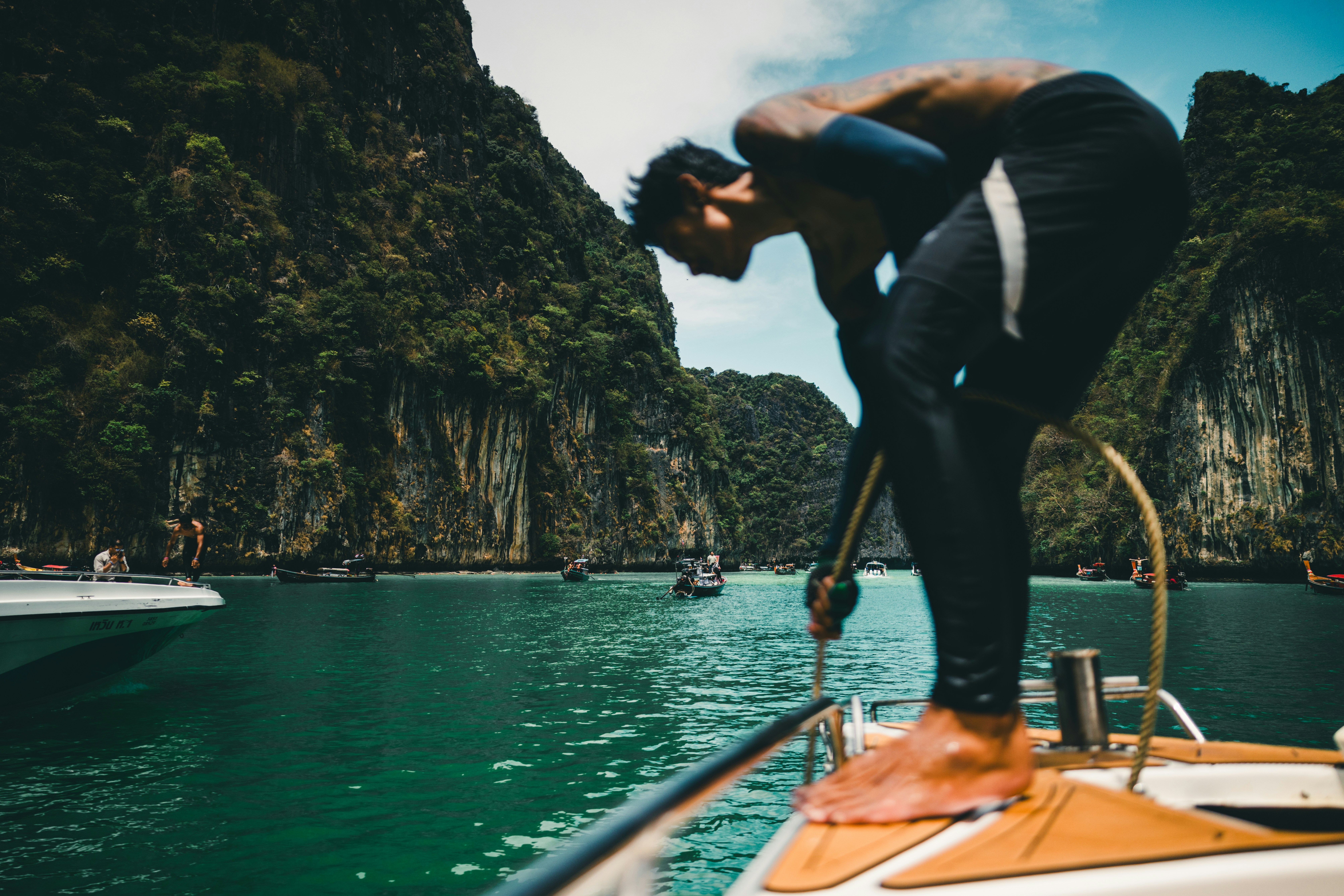 Person on a boat poised with a rope against towering limestone cliffs over turquoise waters.