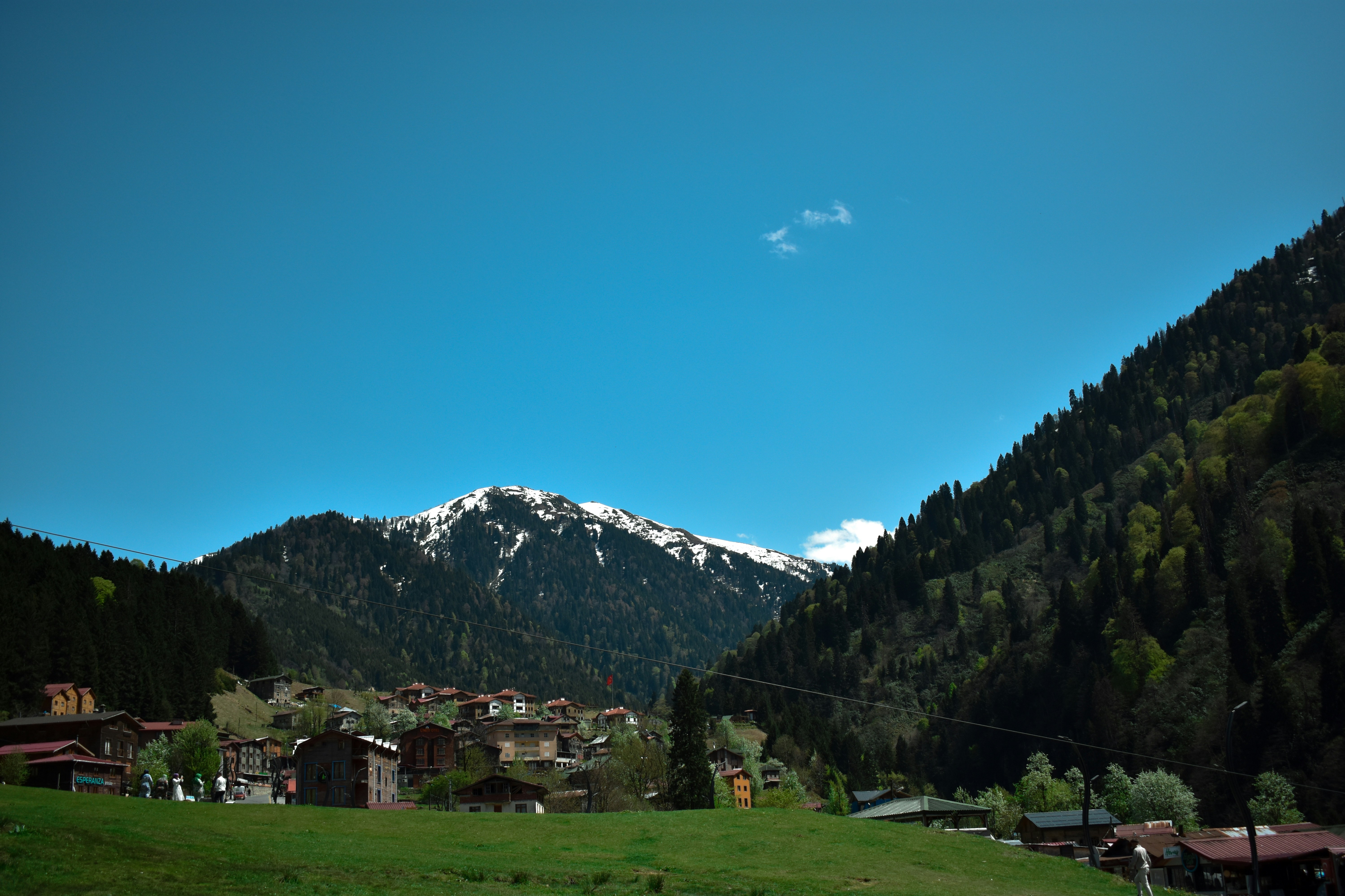 Mountain village nestled in a lush valley with snow-capped peaks under a clear blue sky.