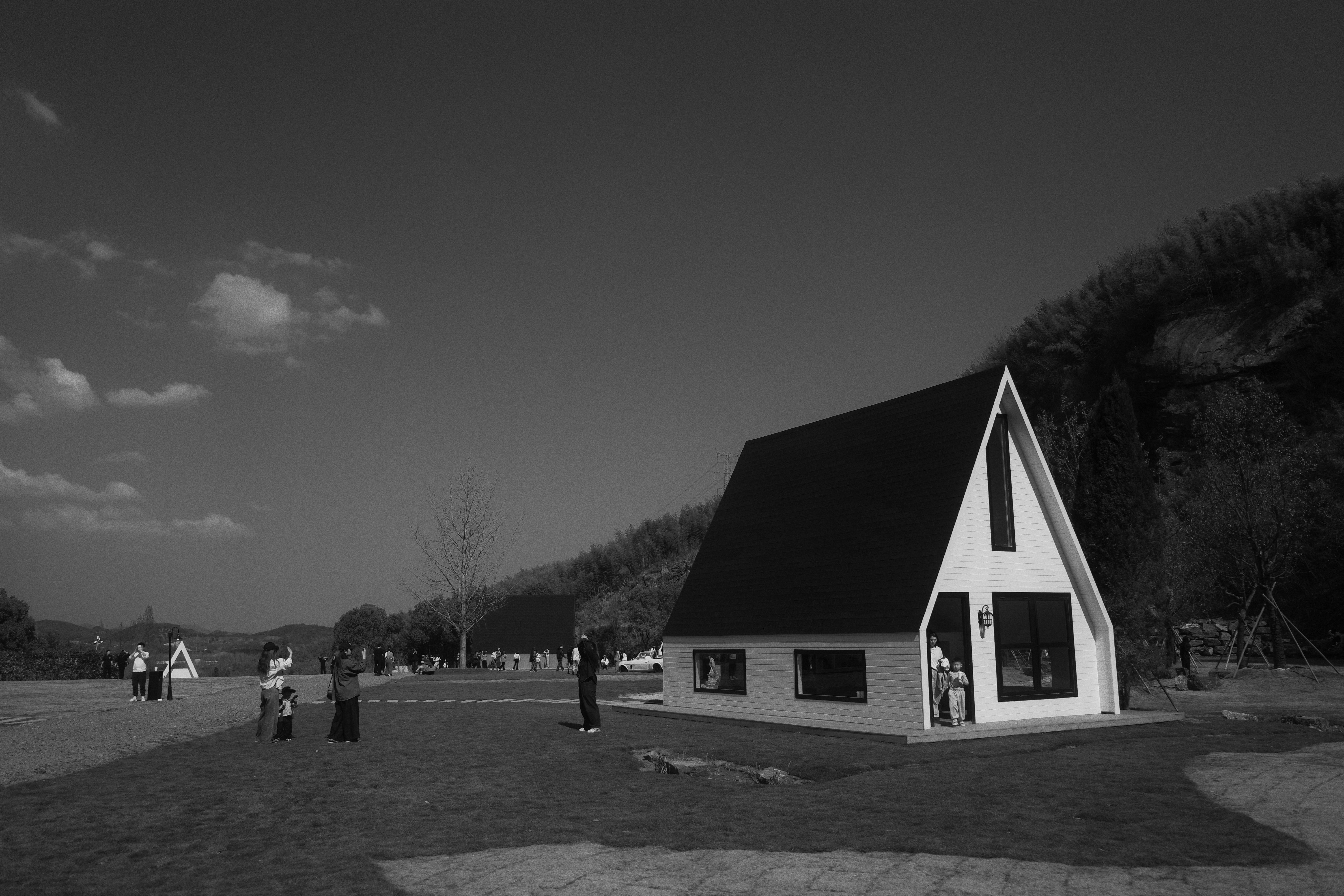 A-frame house surrounded by people in a grassy landscape under a clear sky.