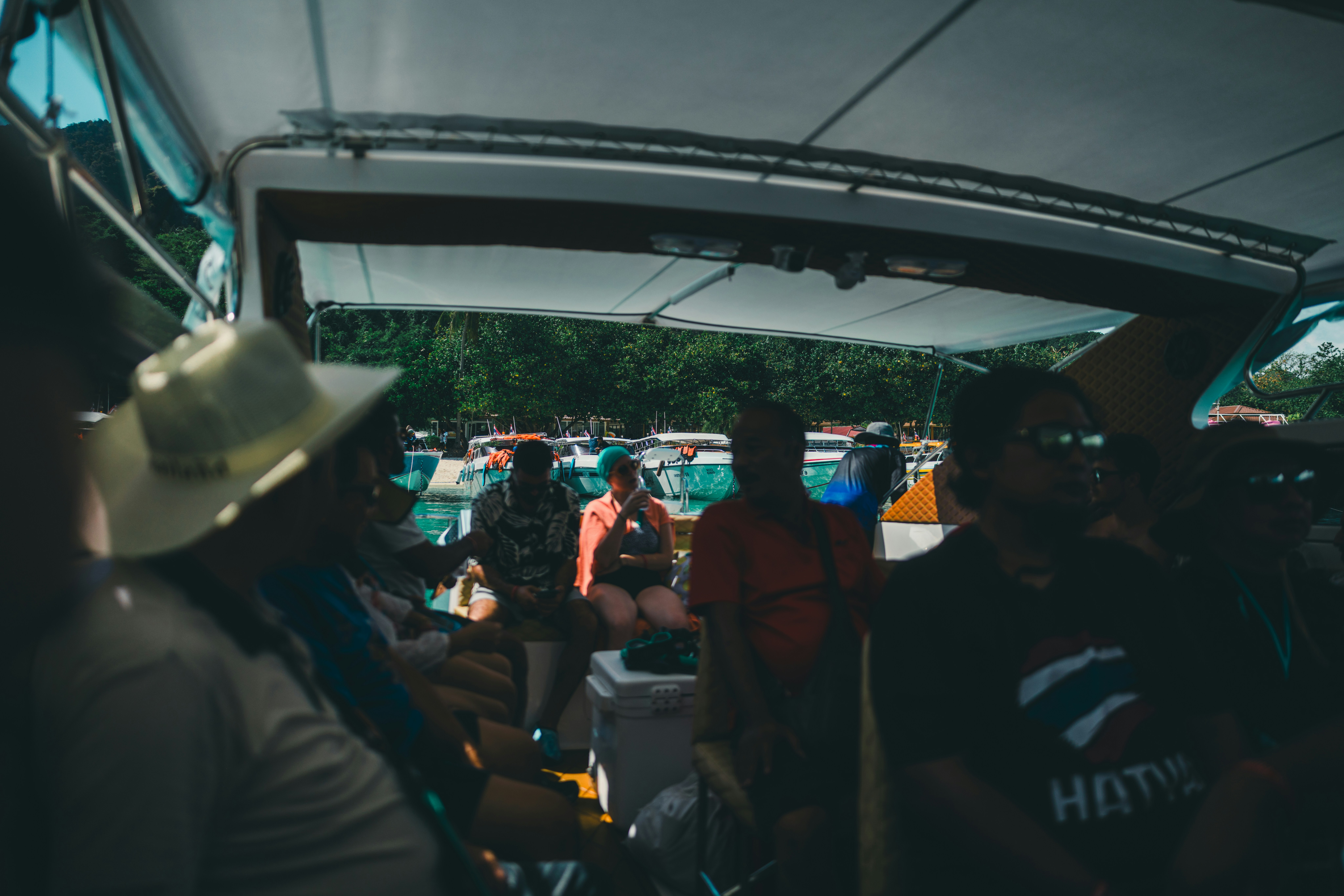 Passengers seated inside a shaded boat surrounded by vibrant green waters and distant boats under a clear sky.