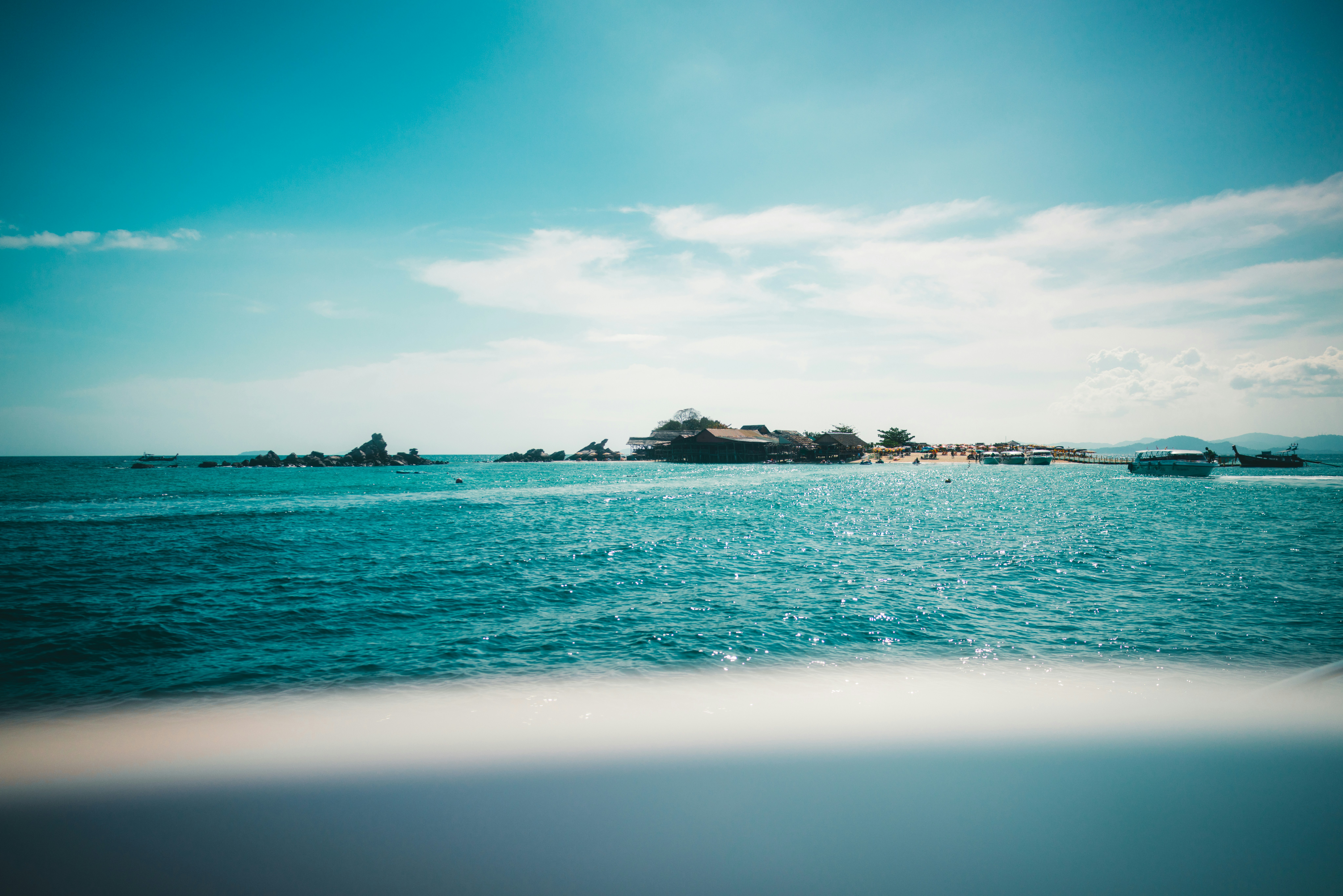 Tranquil ocean scene with a distant island and boats under a bright blue sky.