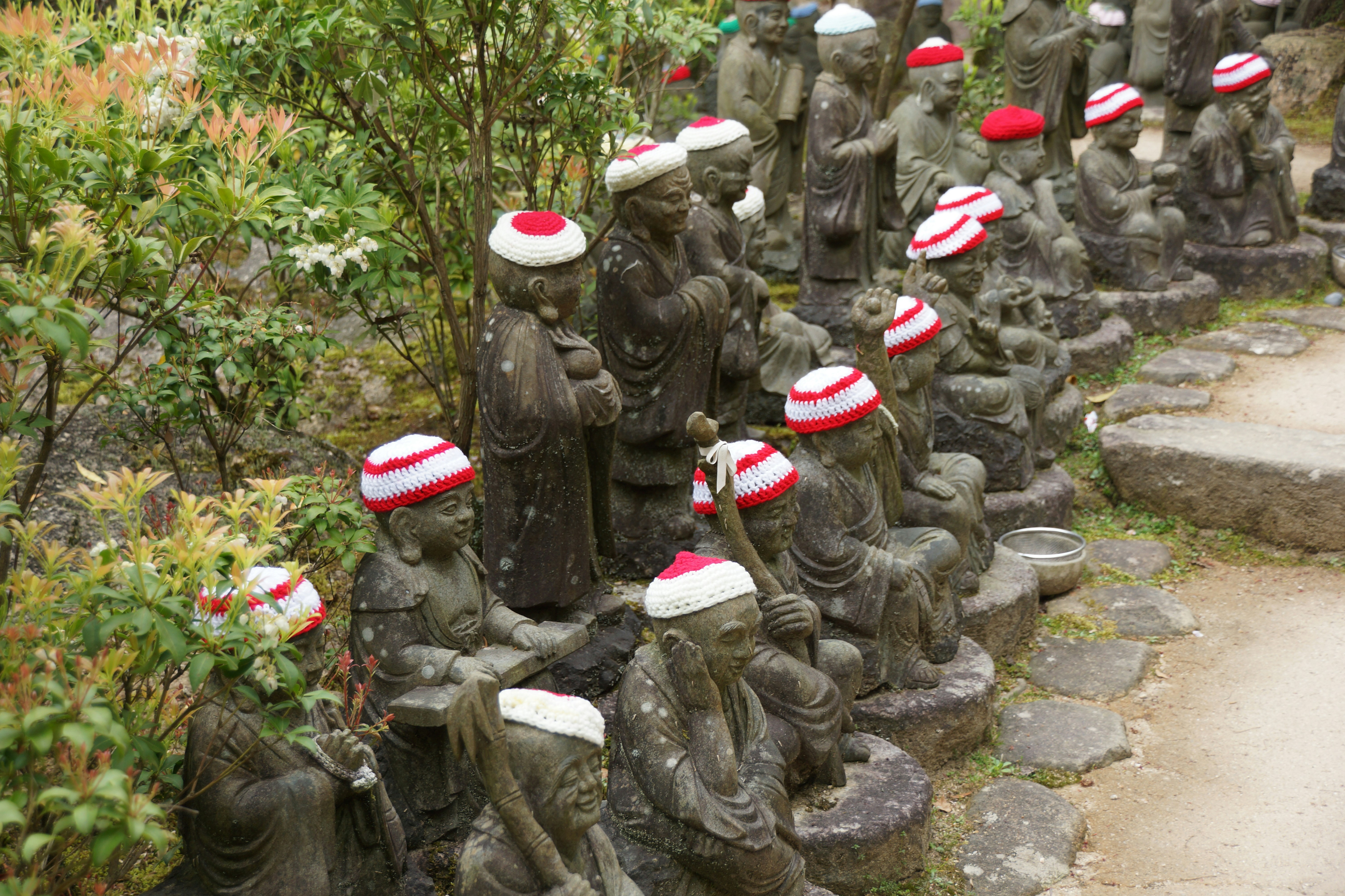 Row of stone statues wearing red and white knit hats surrounded by greenery.