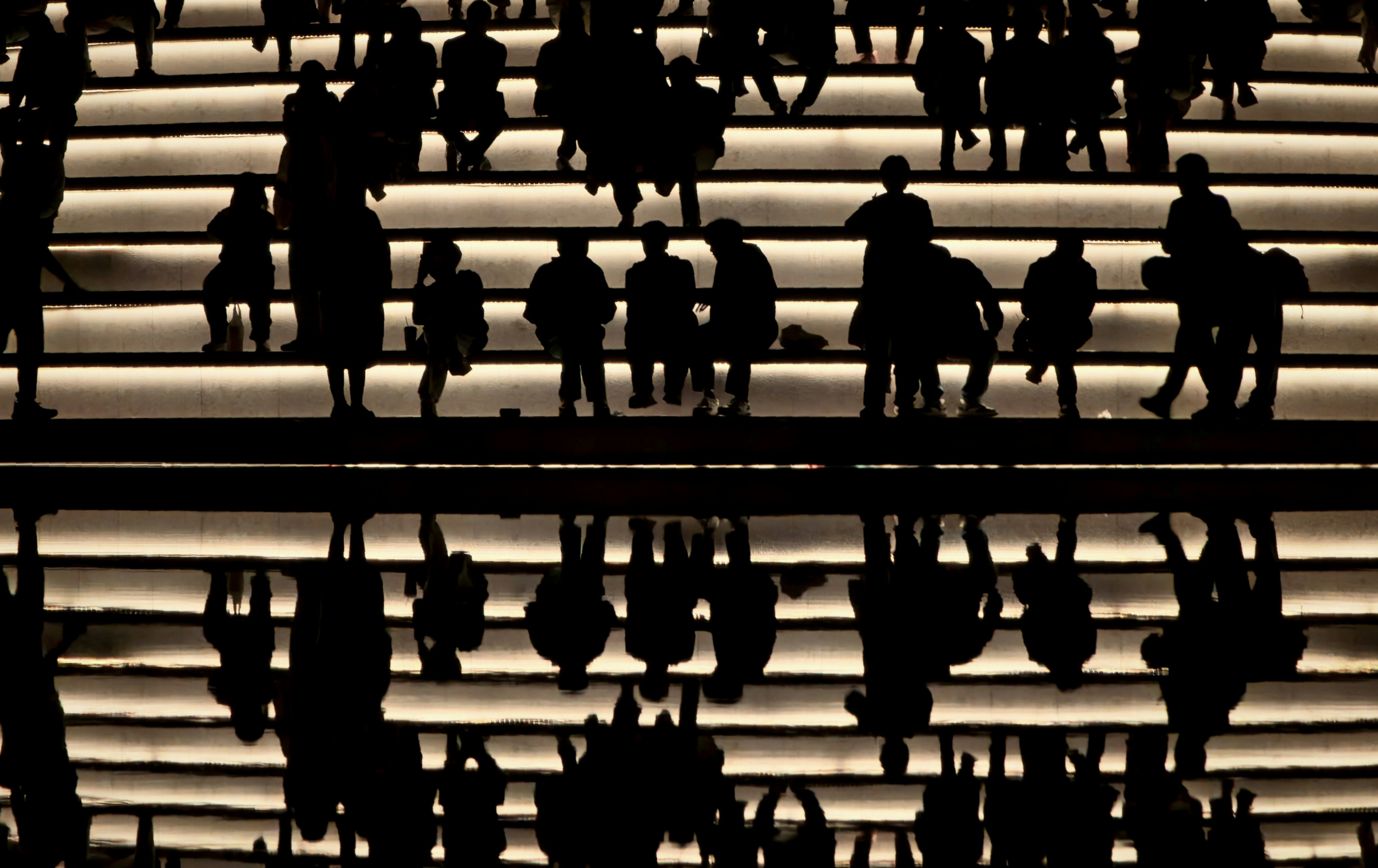 Silhouettes of people on illuminated steps with their reflections below.