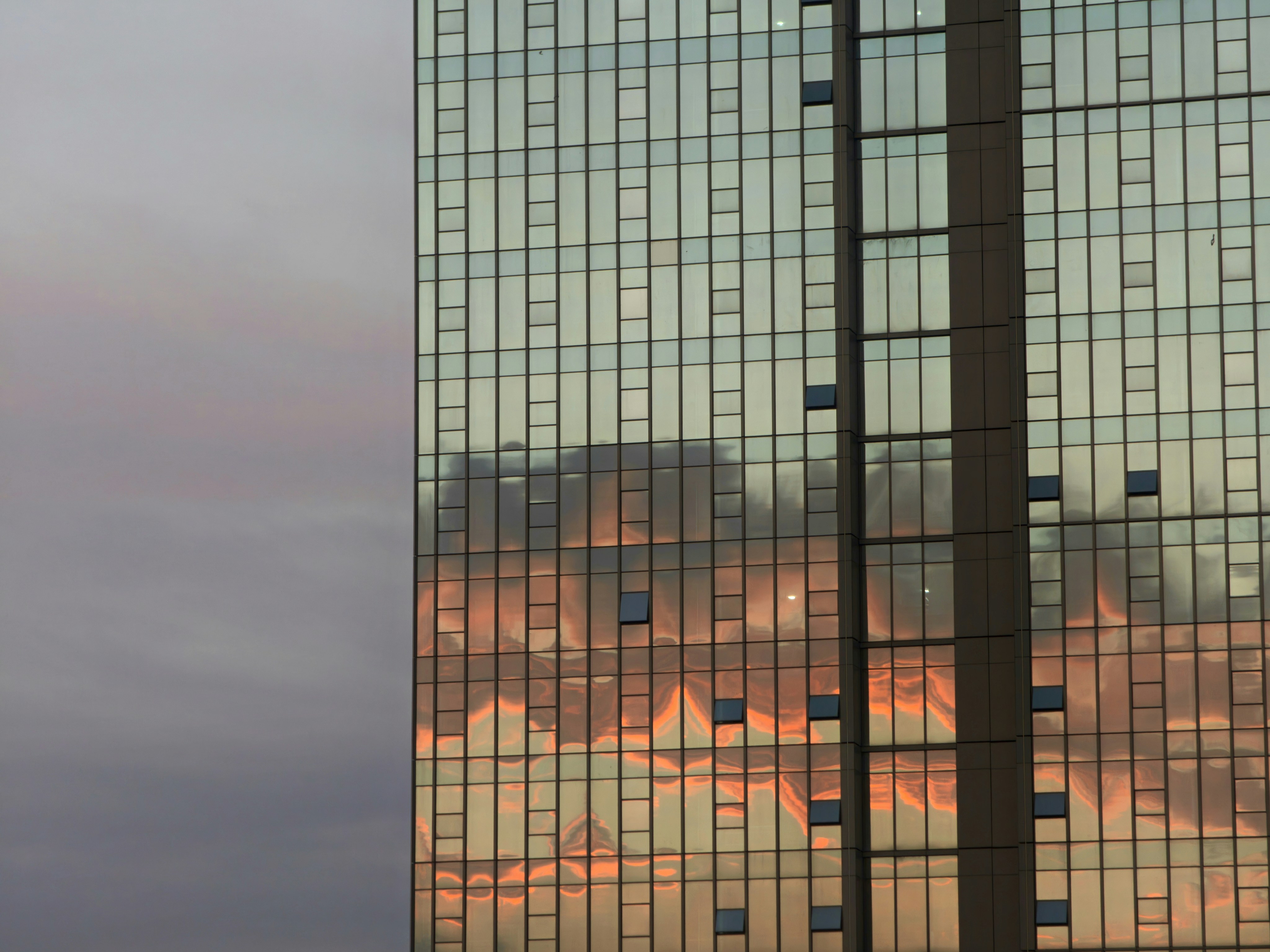 Sunset hues reflecting on a glass skyscraper with a cloudy sky backdrop.