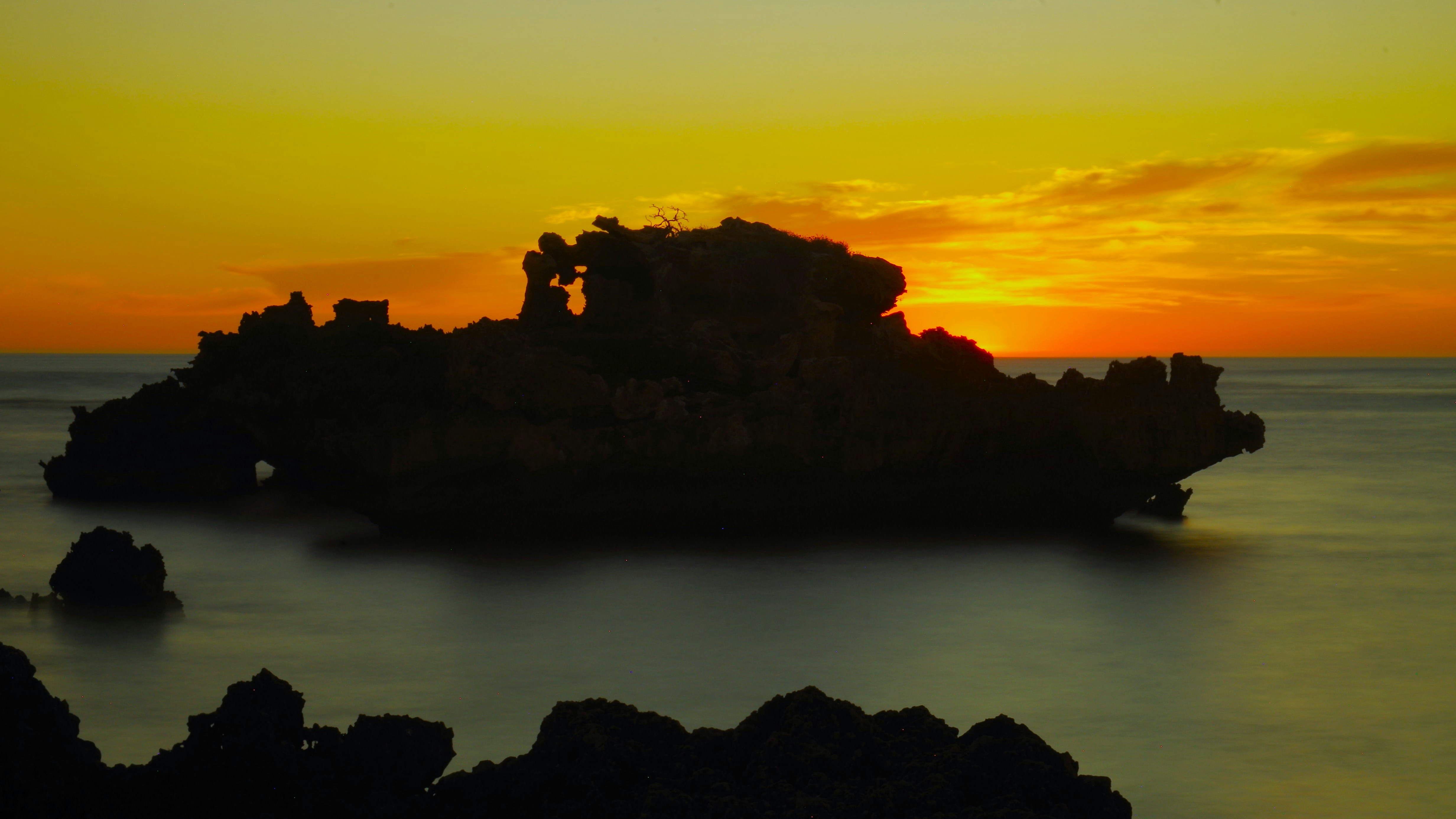 Silhouette of a rugged rock formation against a vibrant coastal sunset.