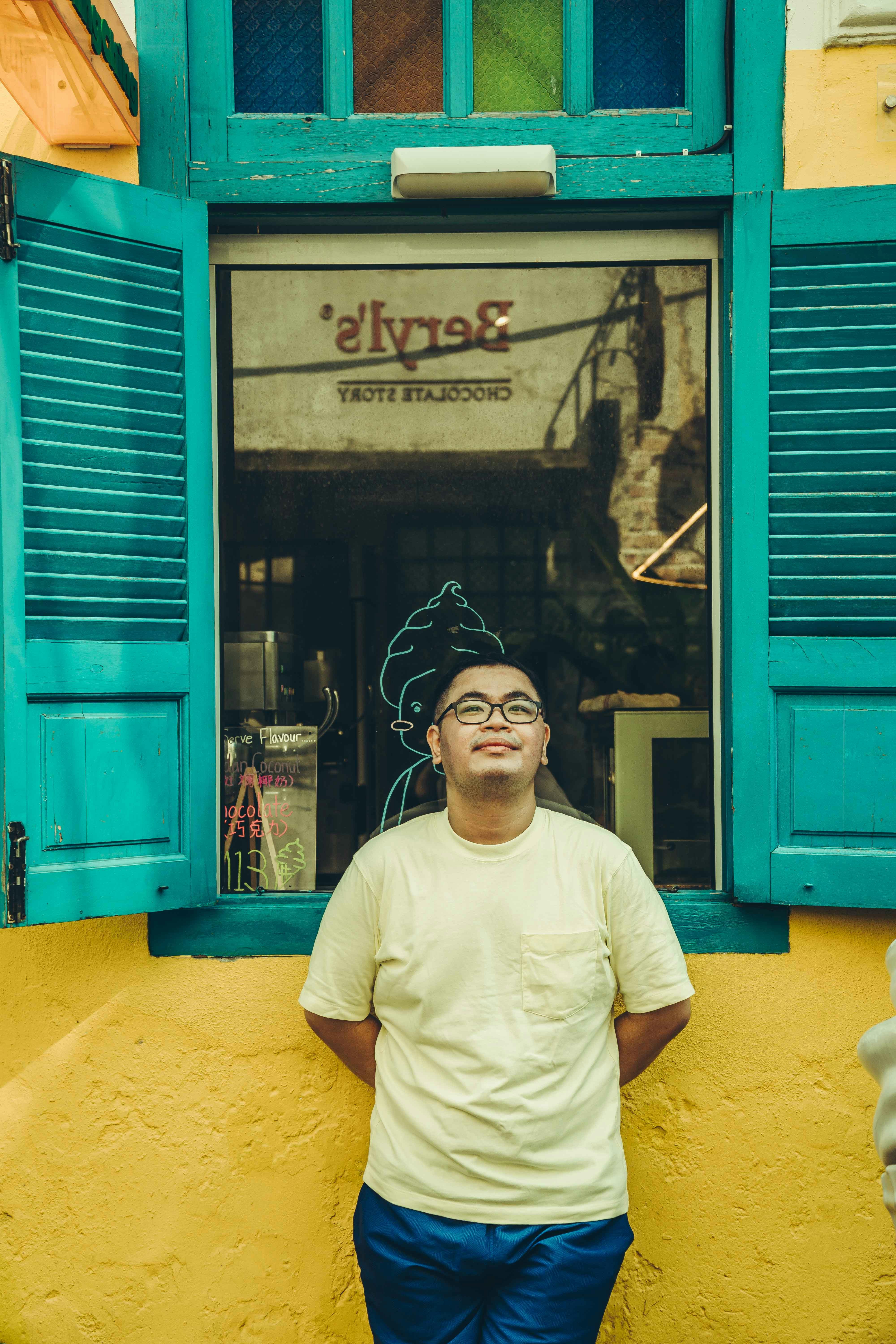 Bright teal doorway frames a calm portrait outside a sunny storefront