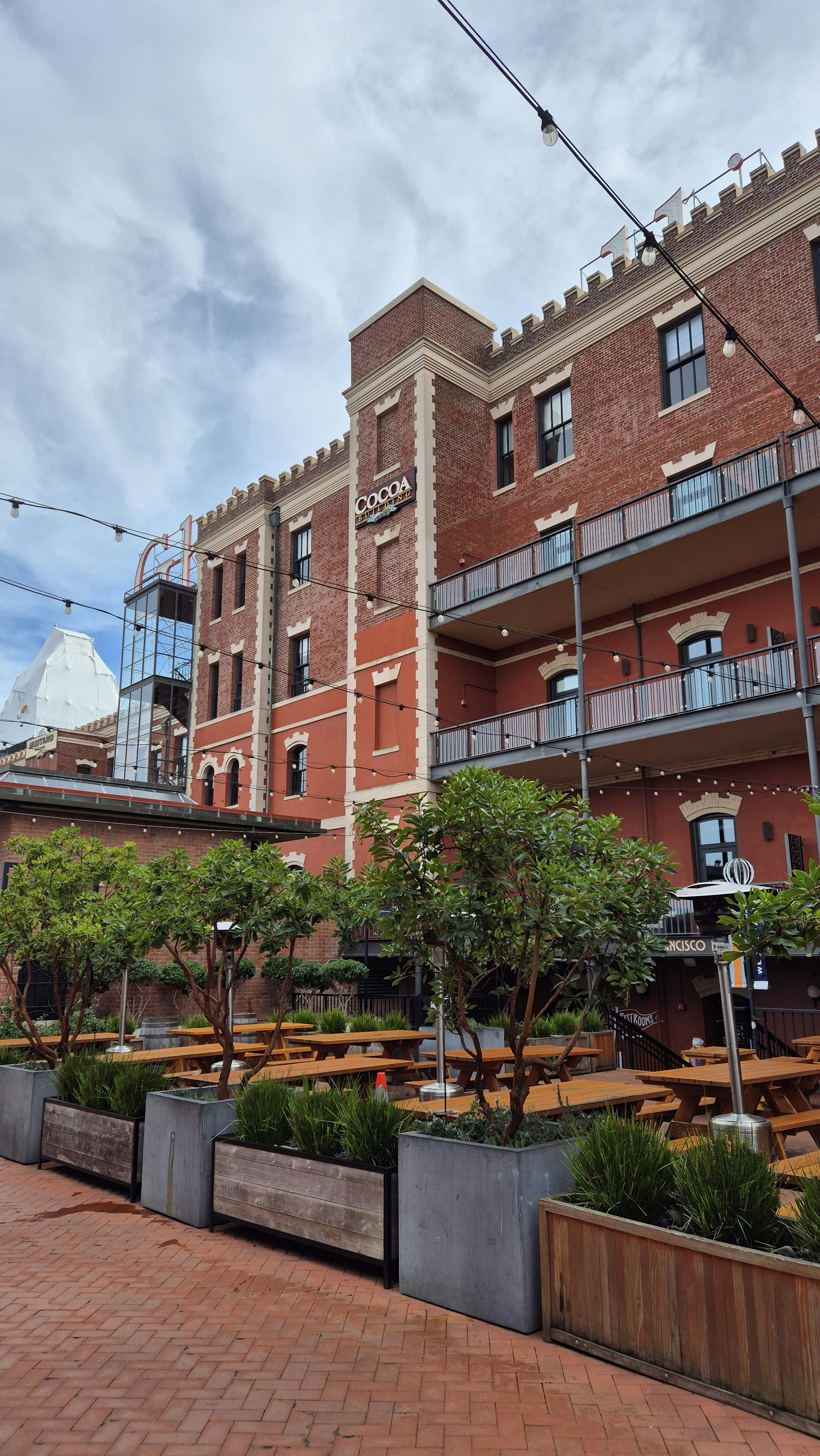 Sunlit Red-Brick Courtyard: Planters, Picnic Tables, and String Lights