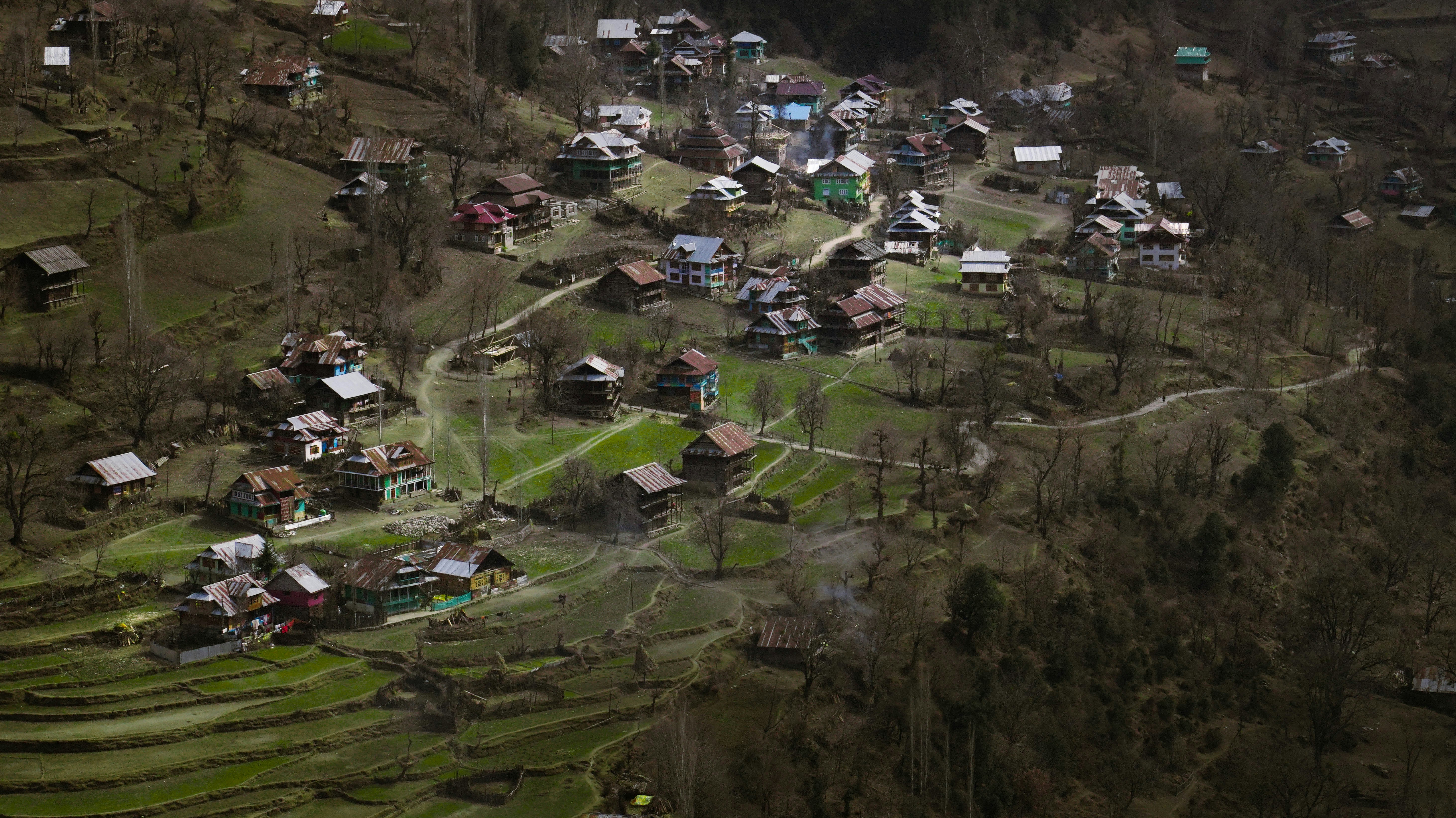 Aerial view of a rural hillside village with scattered houses and lush greenery.