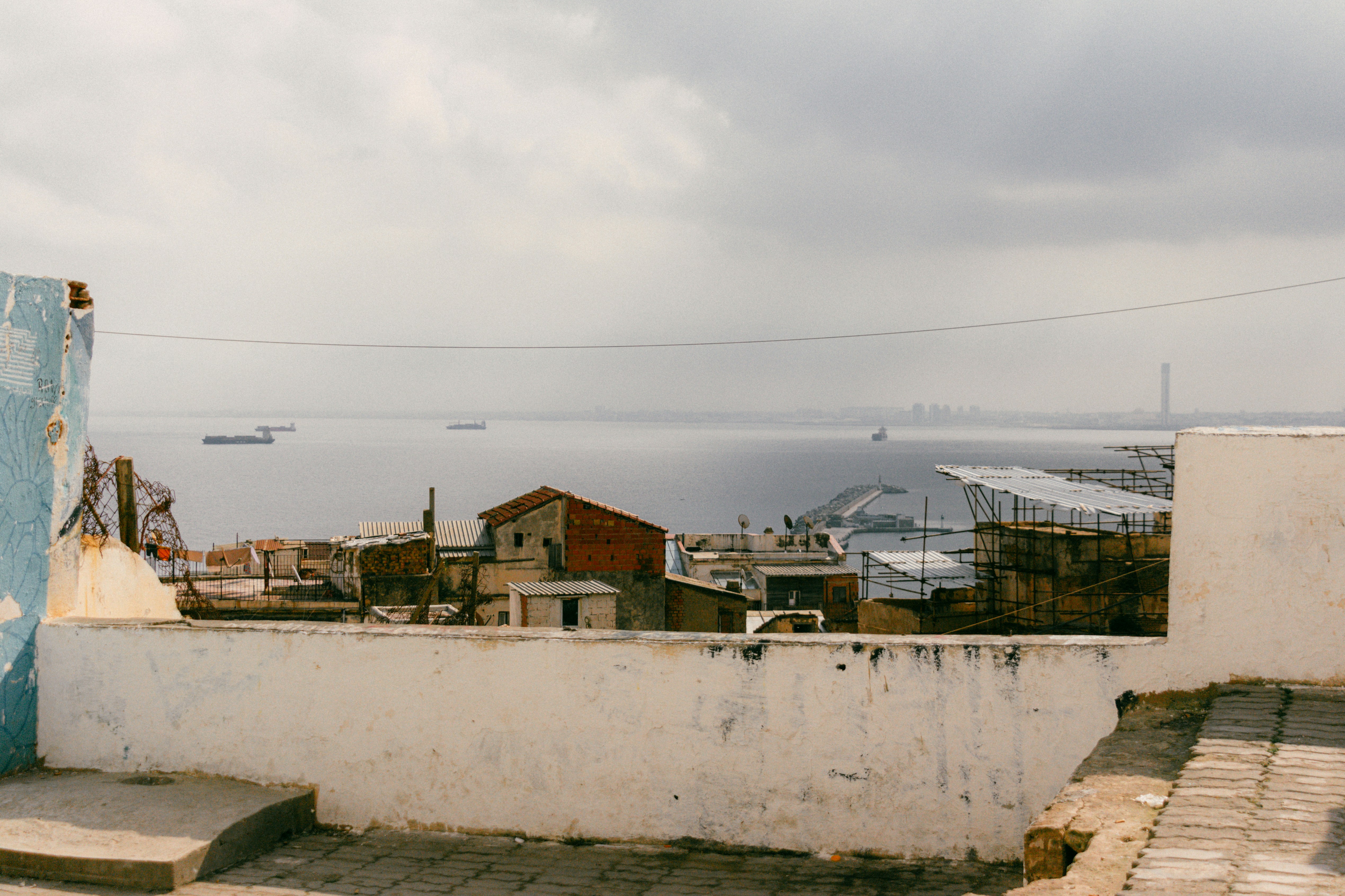 Coastal buildings with flat rooftops overlook the sea under a cloud-filled sky.