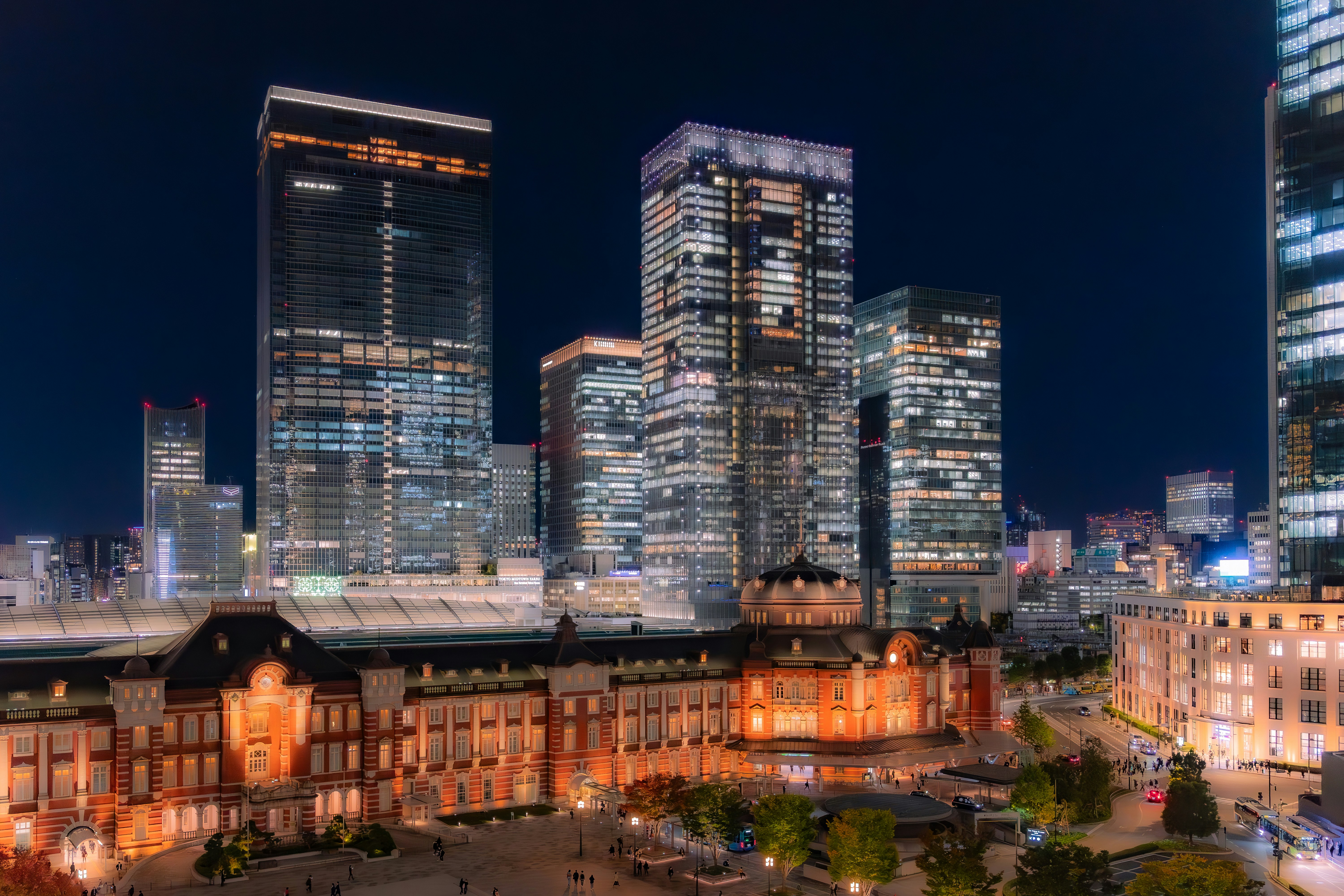 Illuminated skyscrapers tower over the historic Tokyo Station at night.