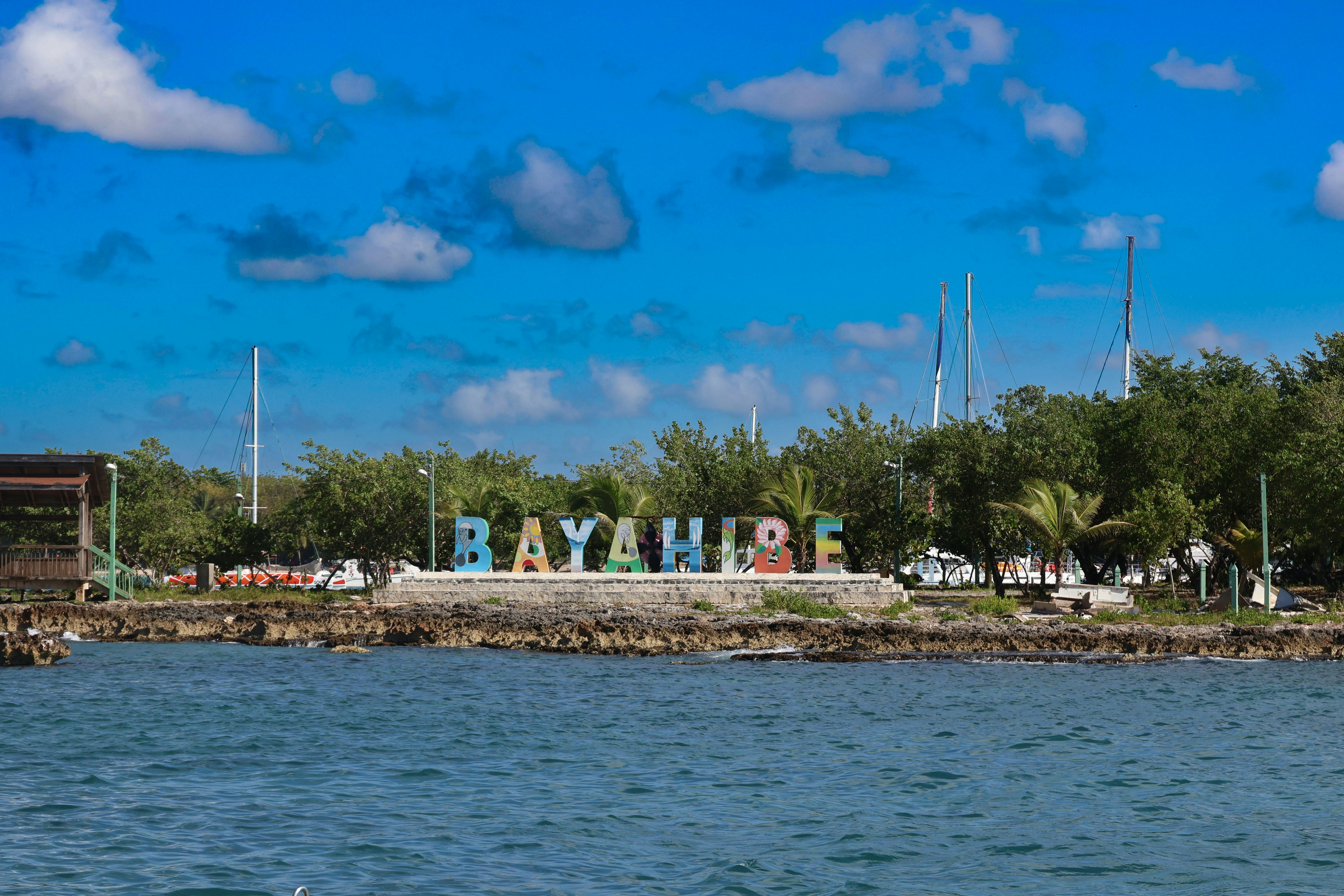 Colorful 'BAYAHIBE' sign by the waterfront, surrounded by lush greenery and a clear blue sky.