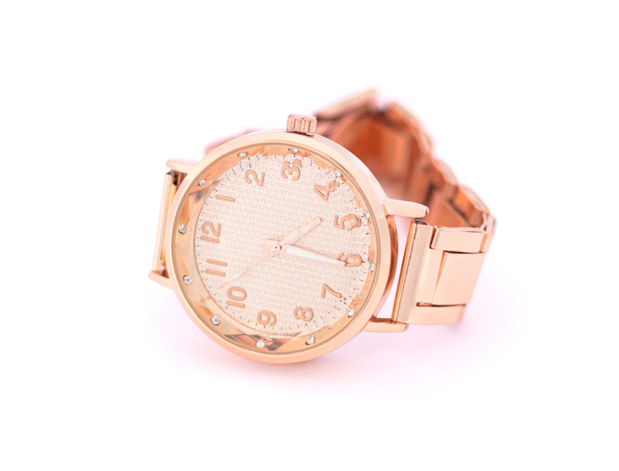 Rose-gold wristwatch with a textured dial and linked metal band, angled on a clean white background. The face and bezel are centered with soft shadowing beneath.