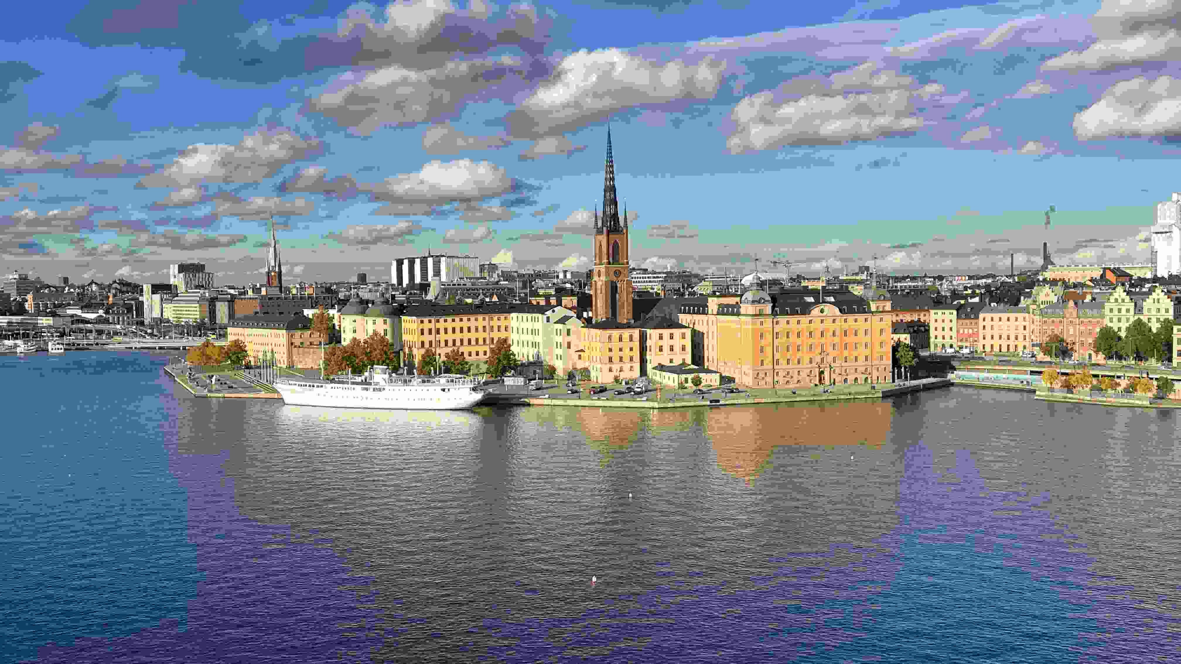Colorful buildings and a church spire reflected in calm waters under a vibrant sky.