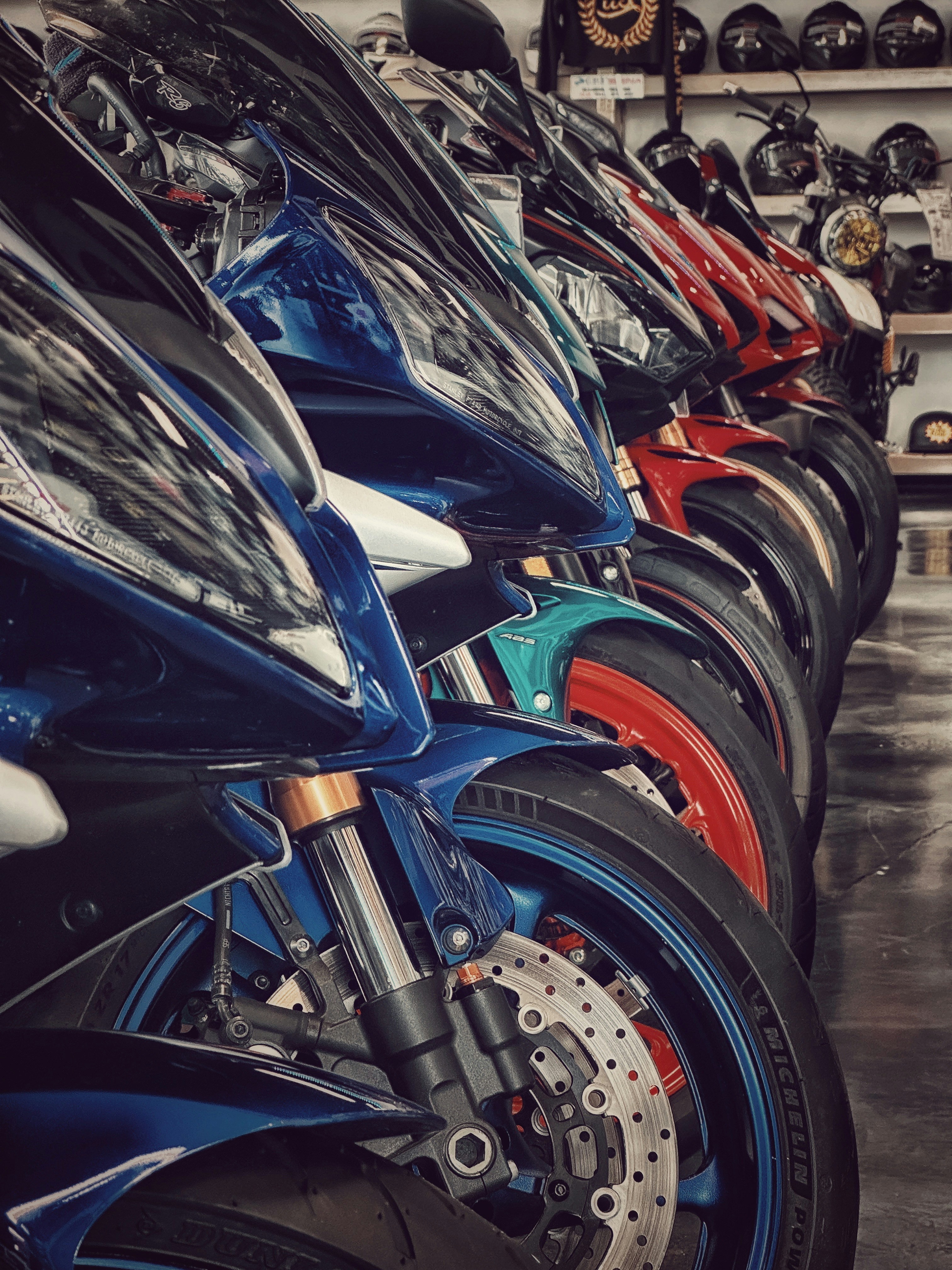 Colorful row of sport motorcycles in a showroom with helmets displayed in the background.